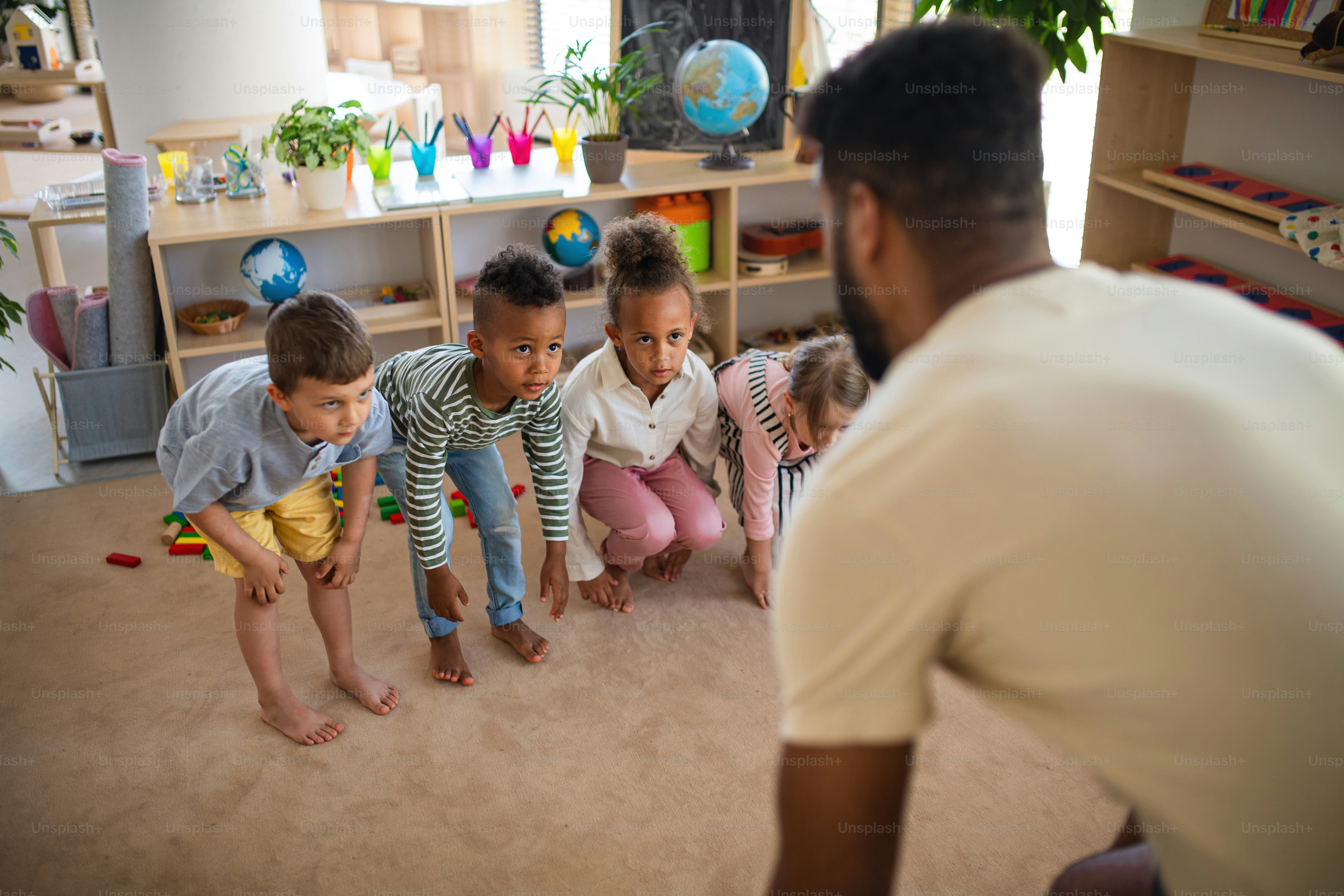 A group of small nursery school children with man teacher sitting on ...