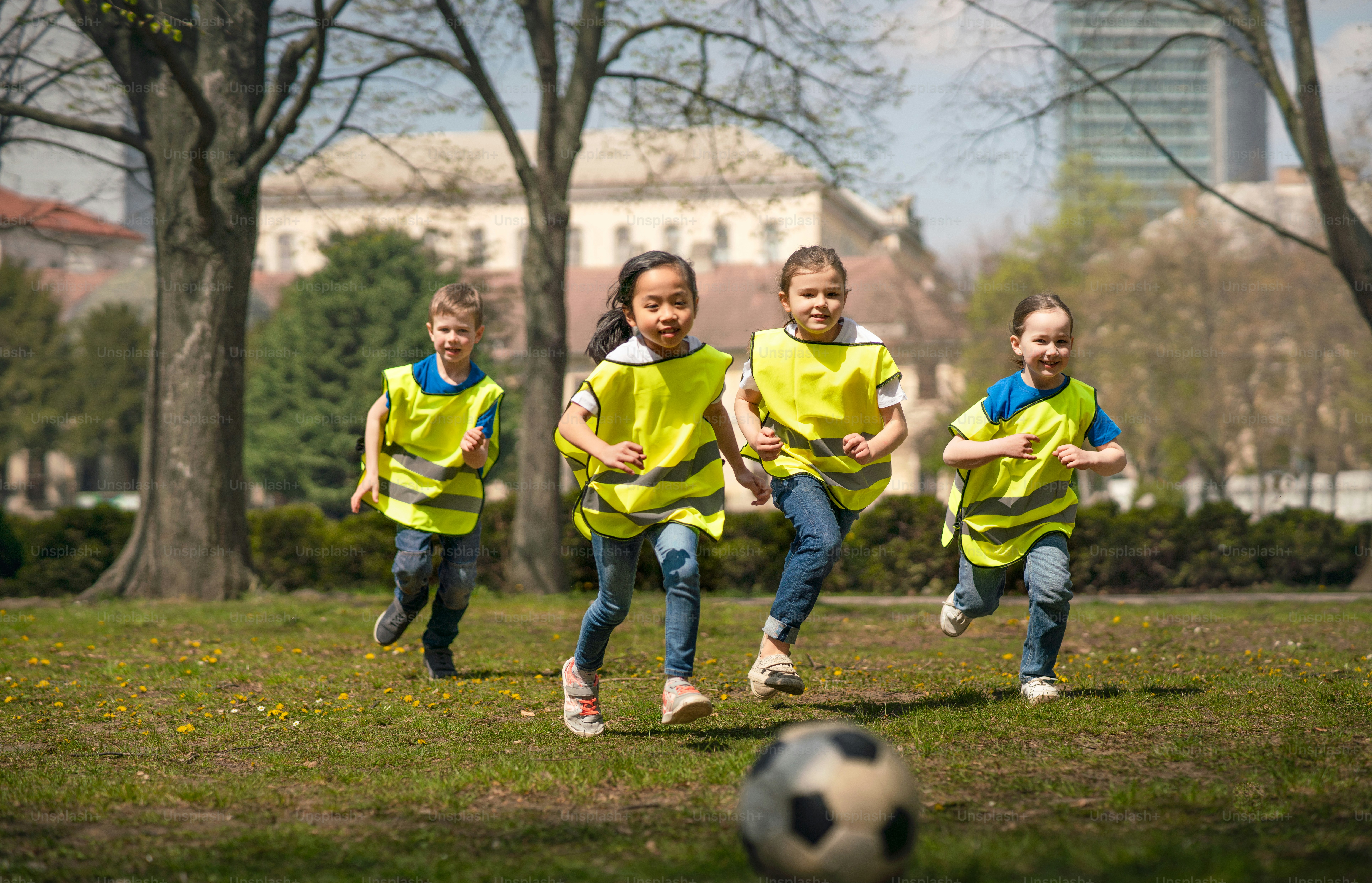 Happy small children playing football outdoors in city park, learning ...