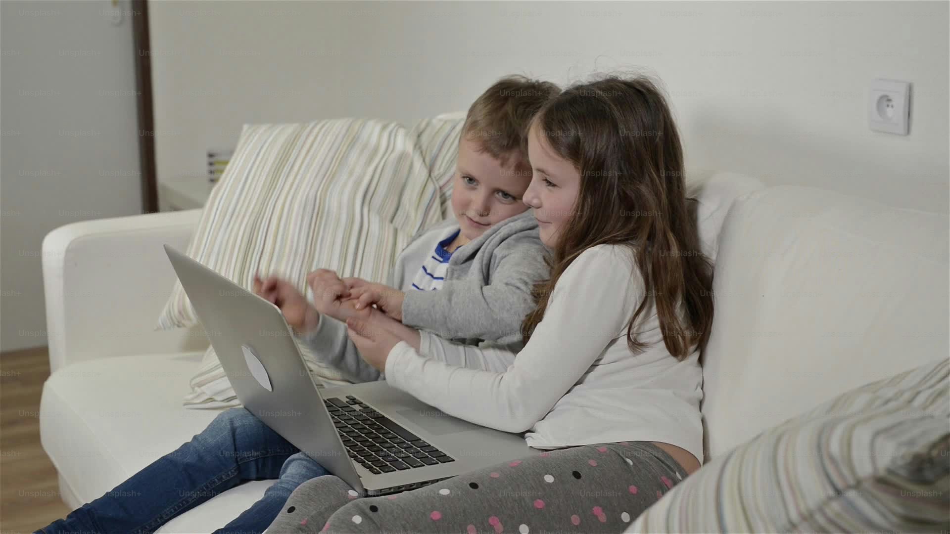 Little girl and boy sitting on sofa with a laptop computer at home ...