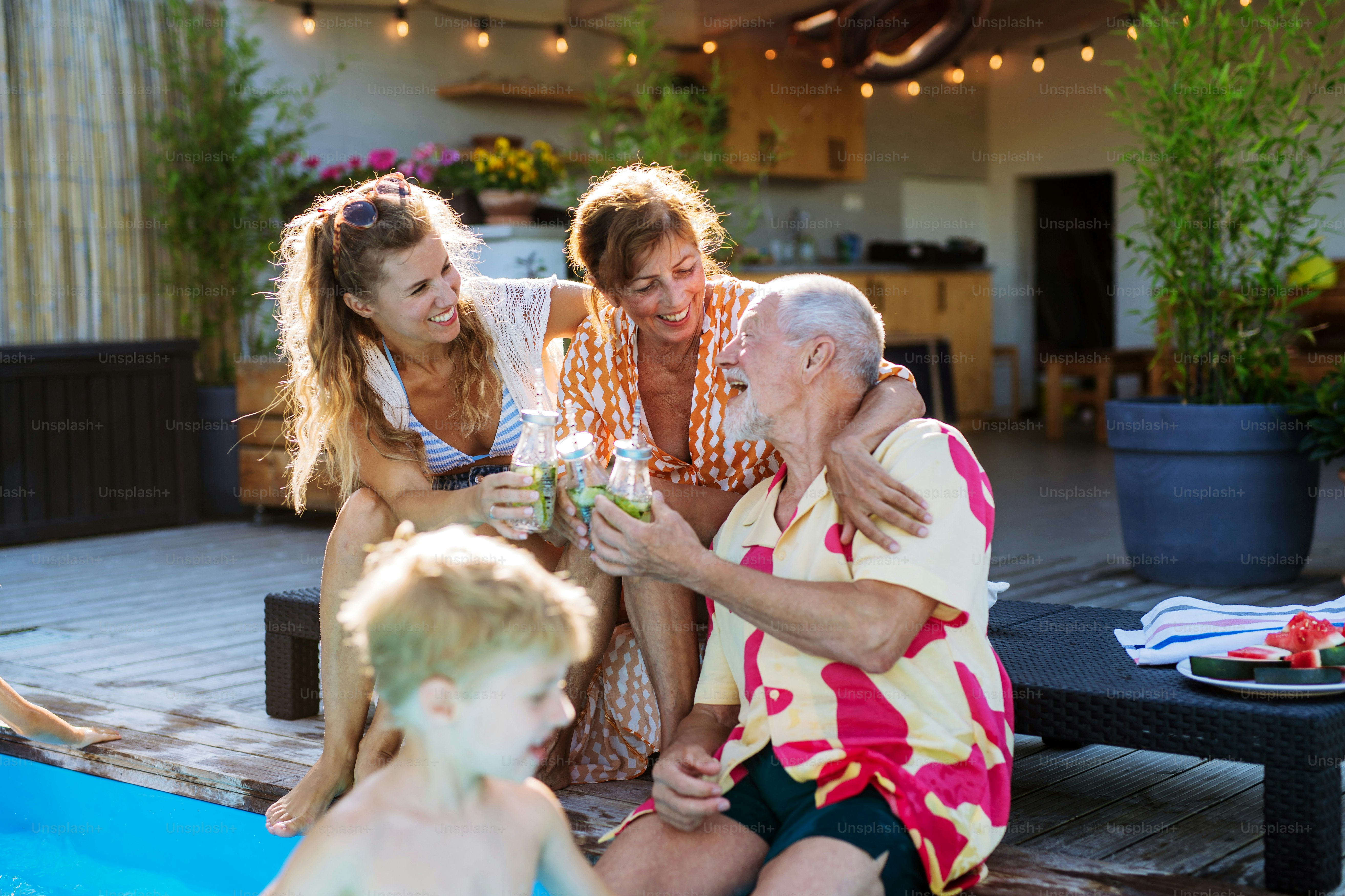 A multi generation family enjoying drinks when sitting at backyard pool ...