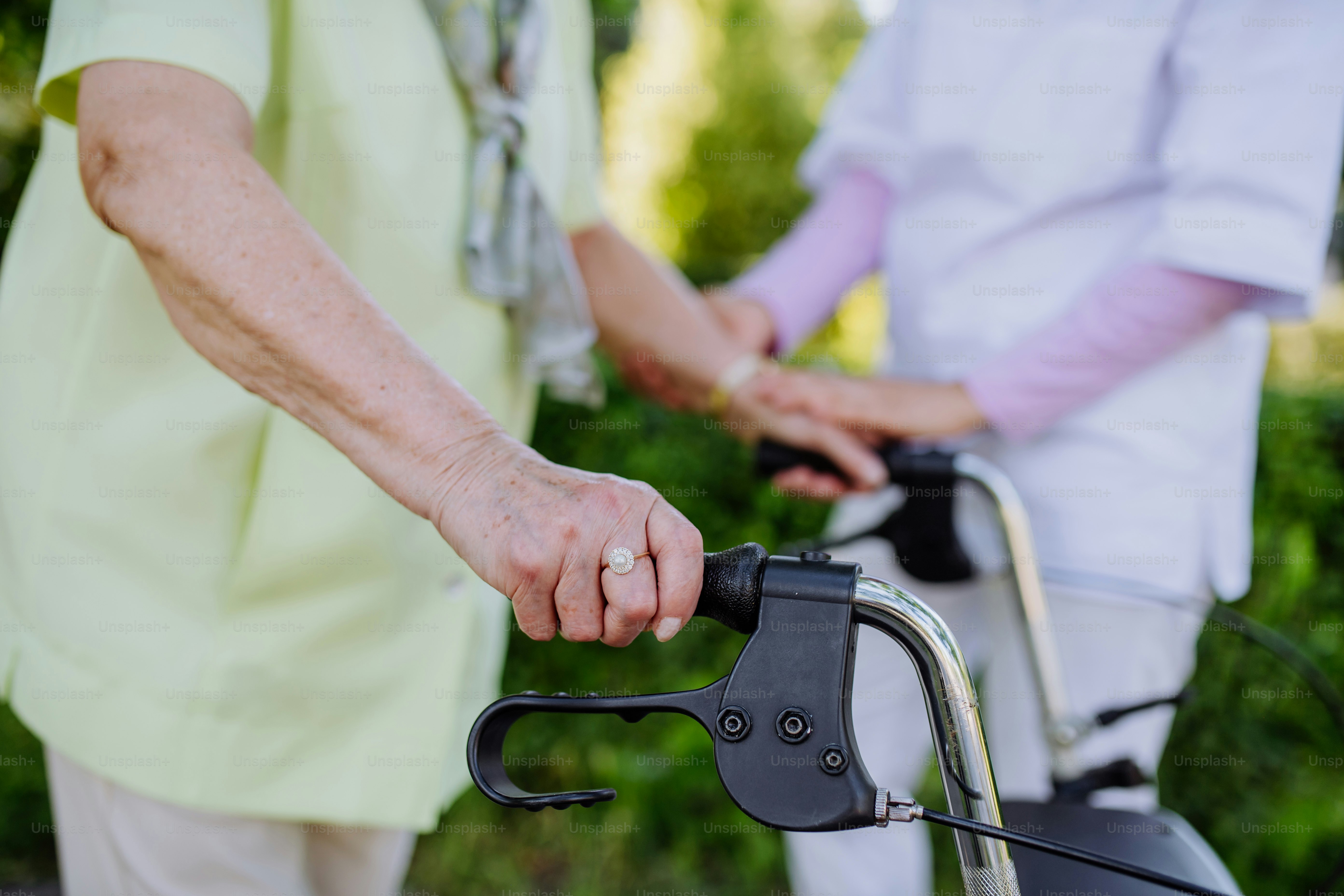 A close-up of caregiver helping senior woman on walk with walker in ...