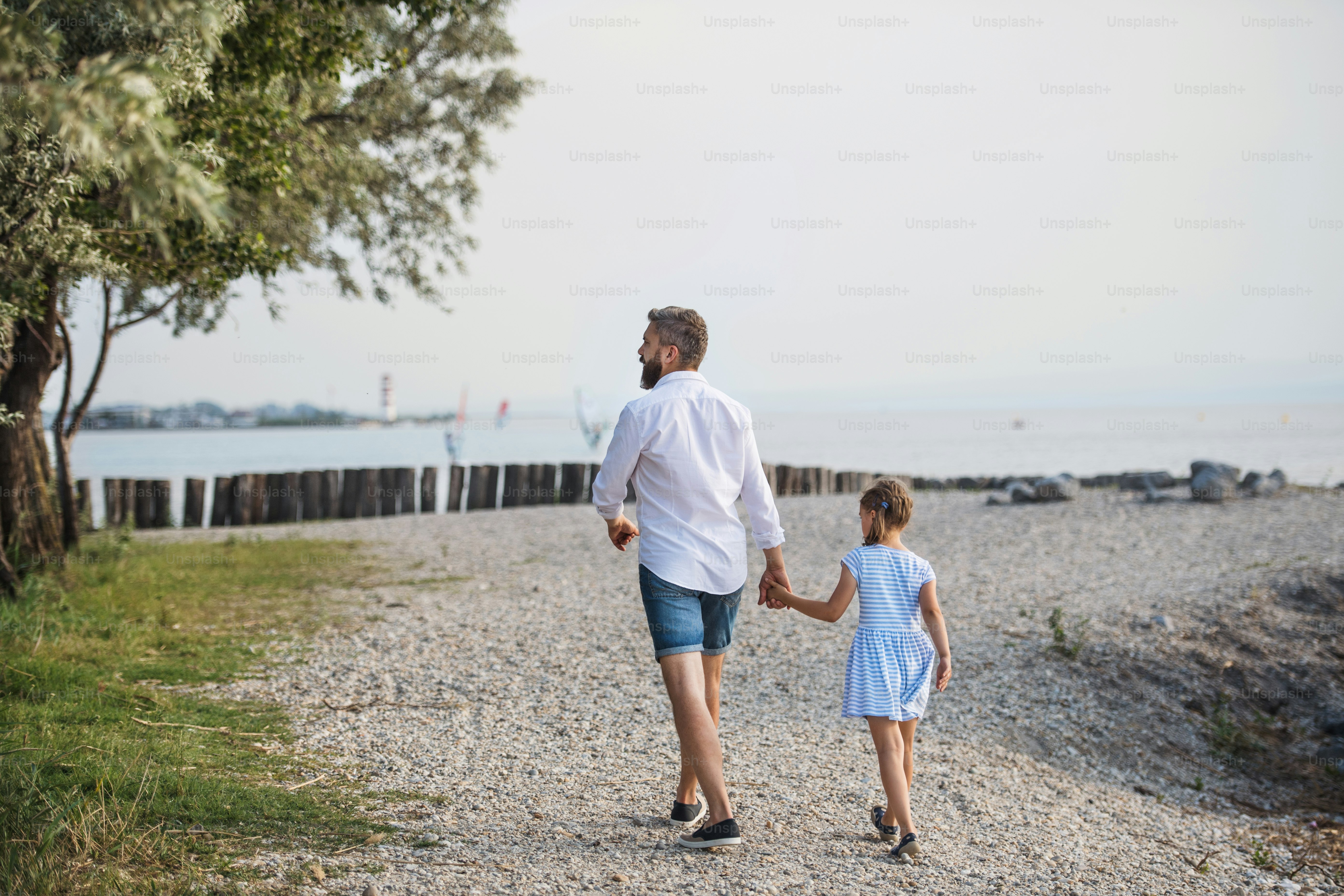 Rear view of mature father walking with small daughter on a holiday by ...