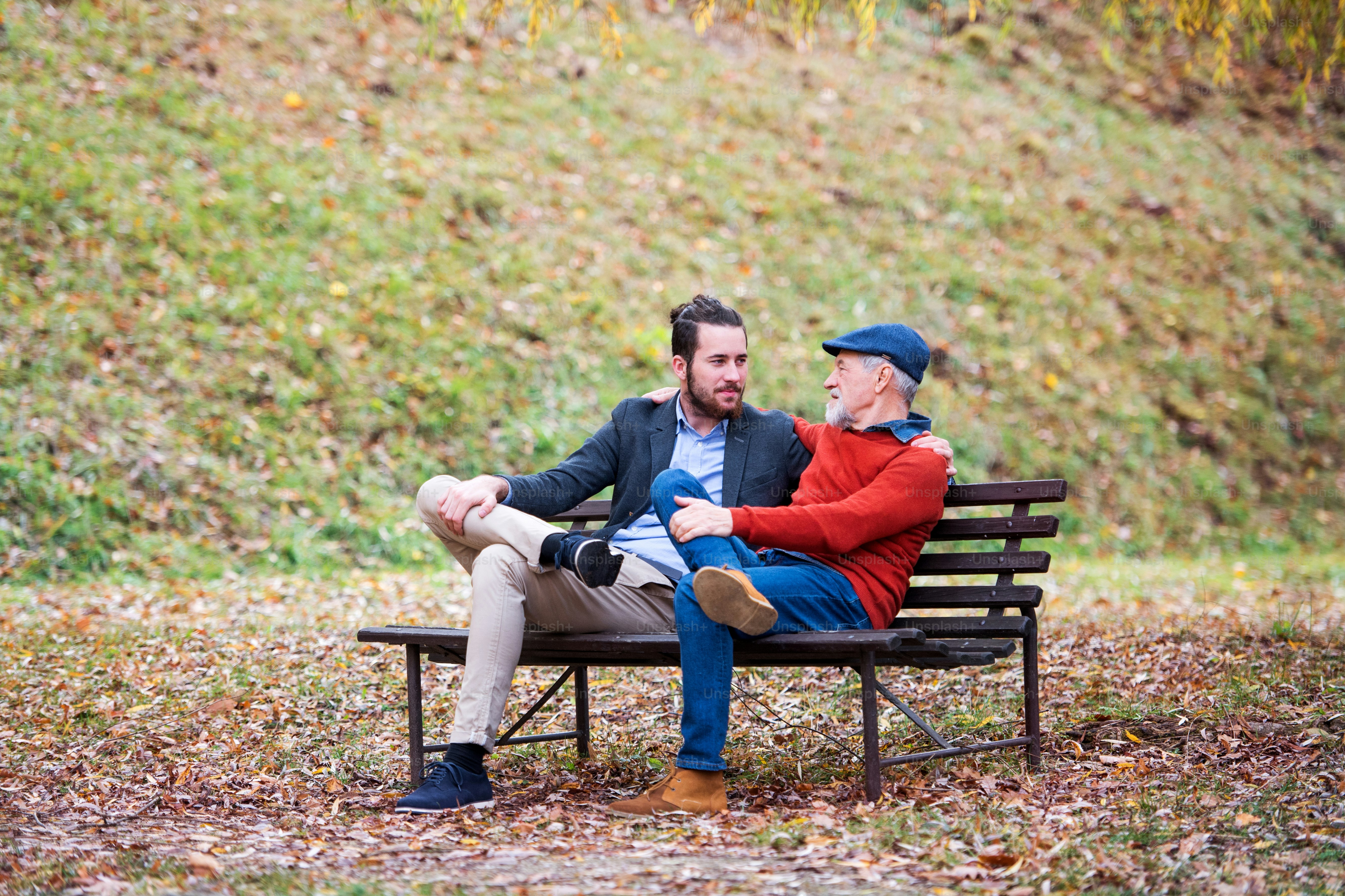 Senior father and his young son sitting on bench in nature, talking ...