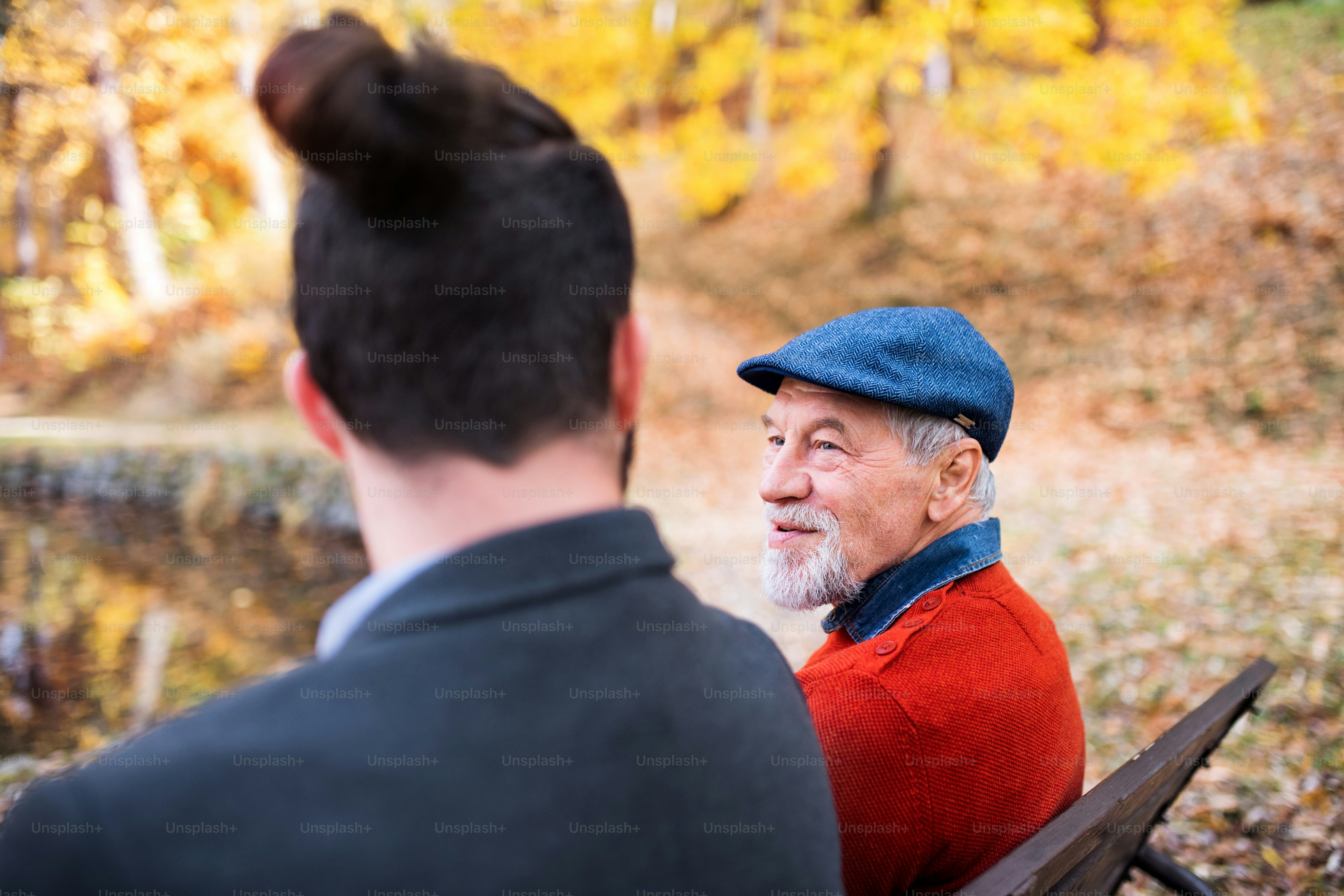 Senior father and his young son sitting on bench by lake in nature ...