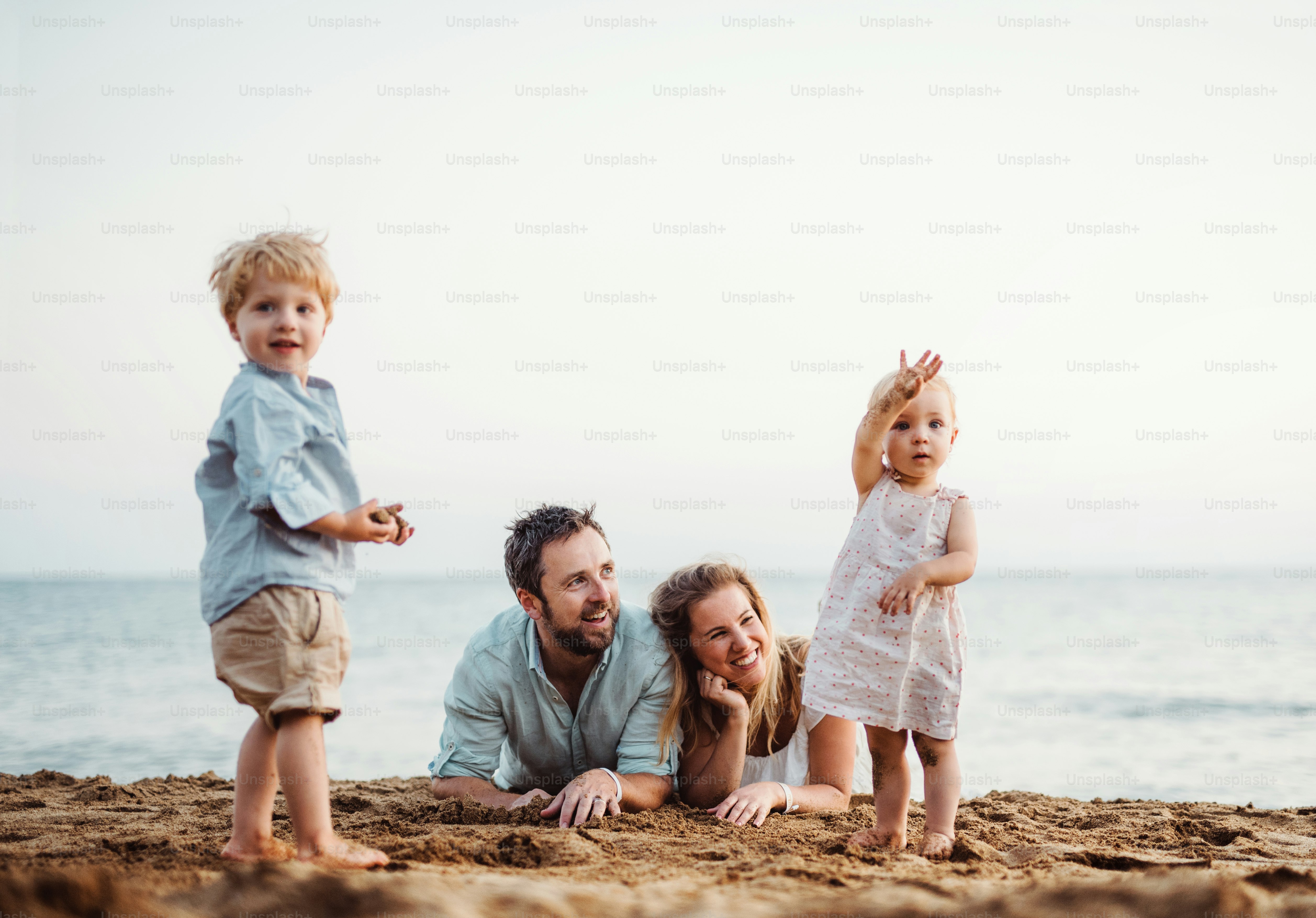 A family with two toddler children lying on sand beach on summer ...