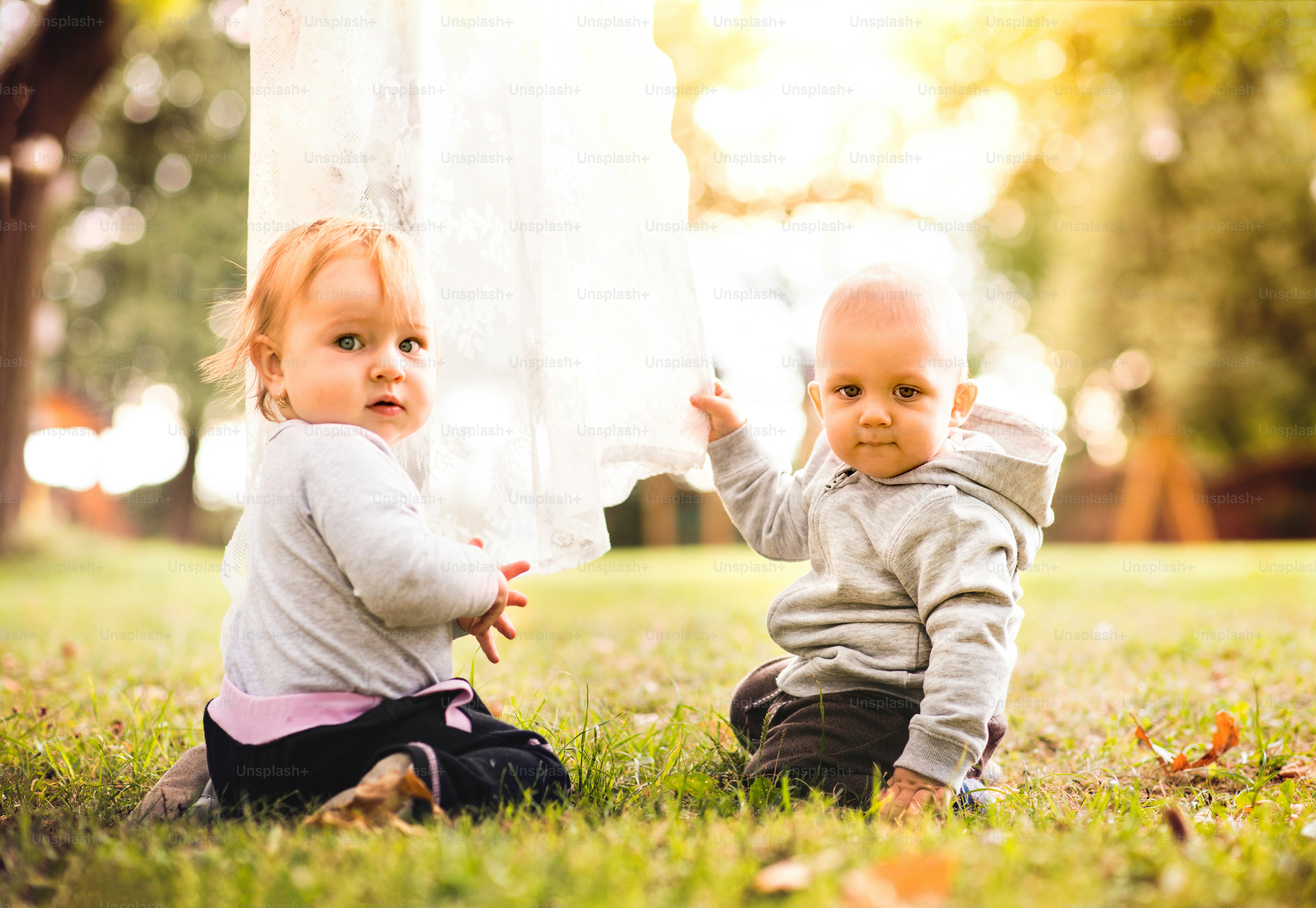 Two babies on the grass in the garden. Baby girl and baby boy sitting ...