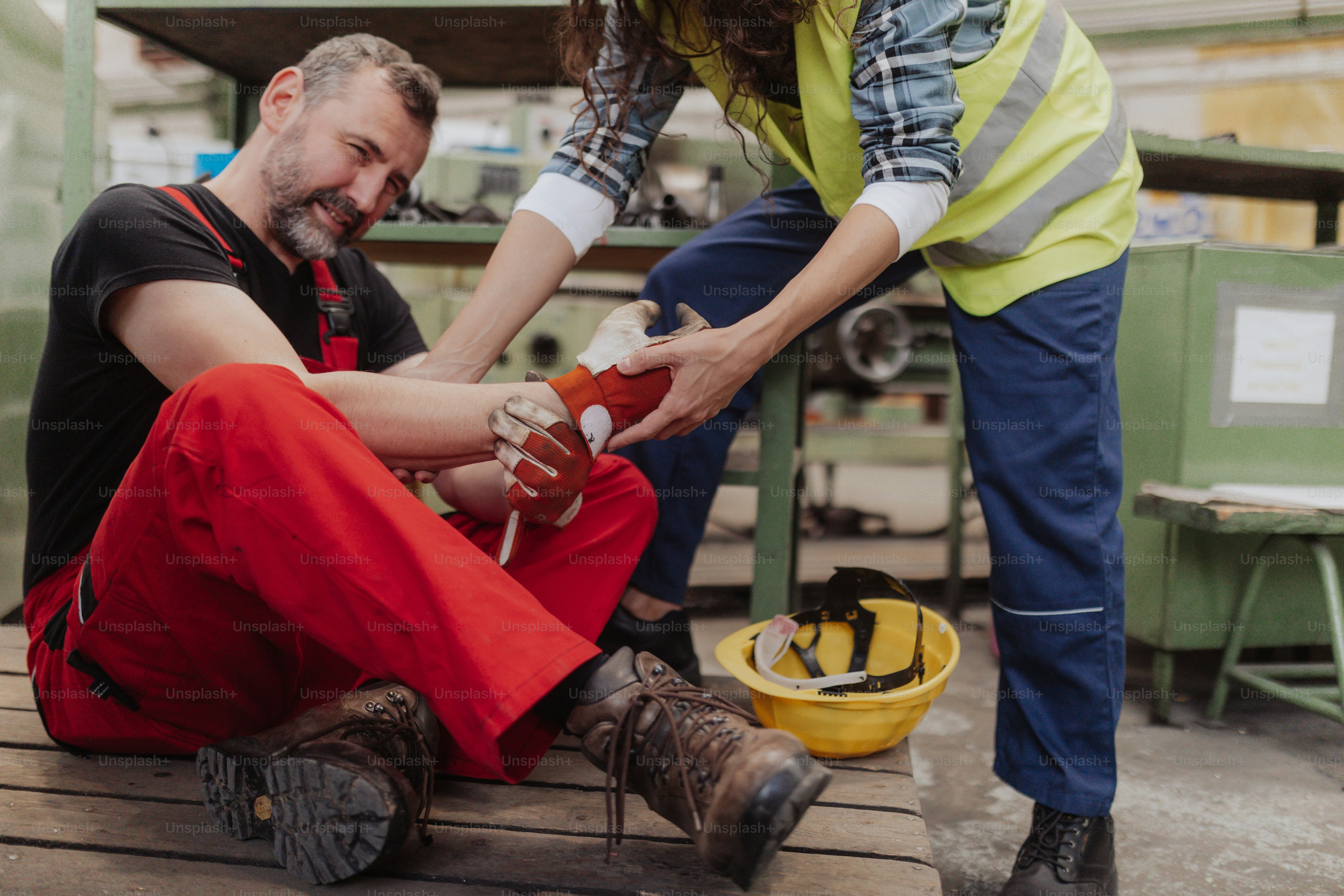 A woman is helping her colleague after accident in factory. First aid ...