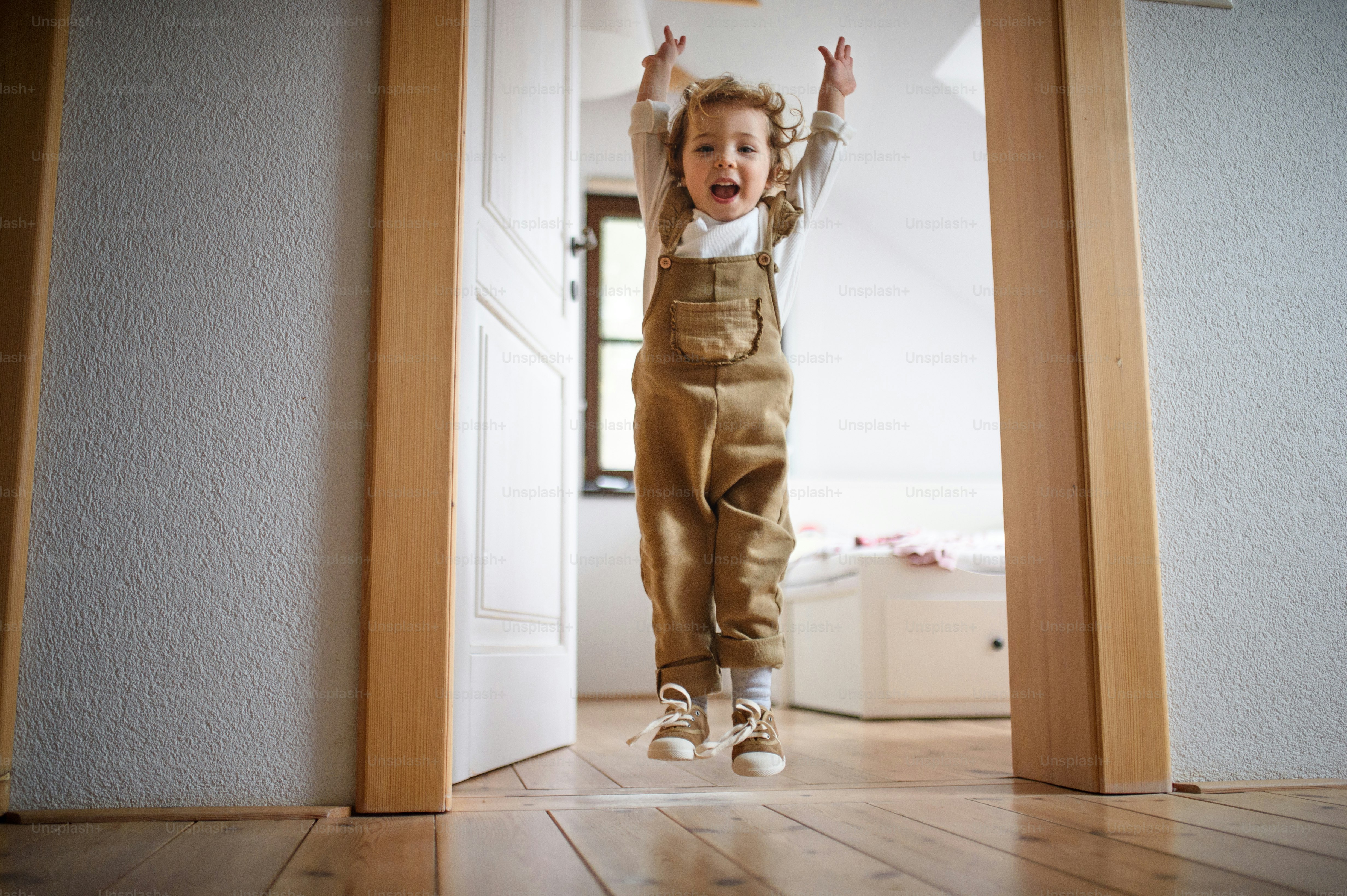 Front view of small toddler girl jumping indoors at home, having fun ...