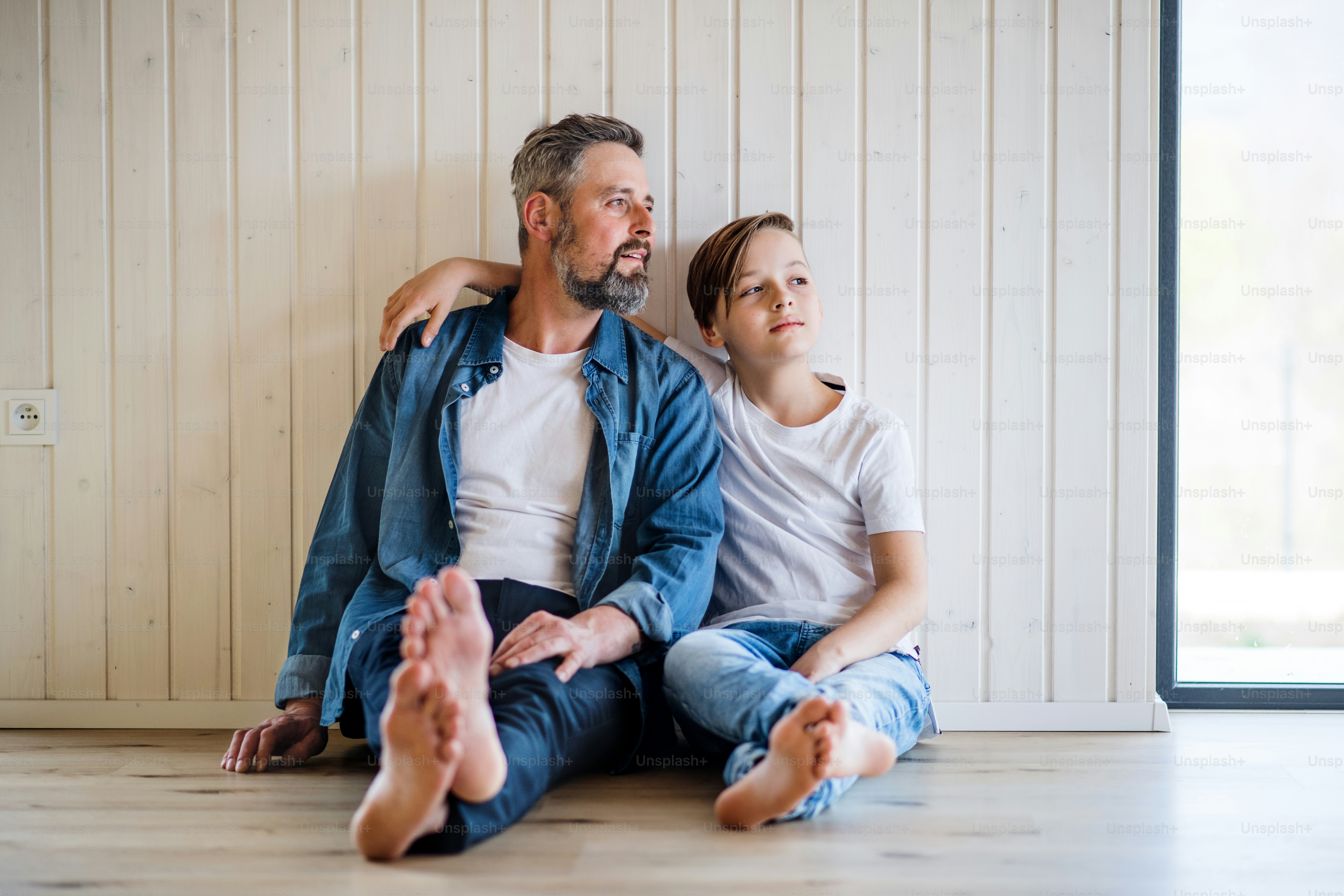 Mature father with small son sitting indoors ont the floor, talking ...