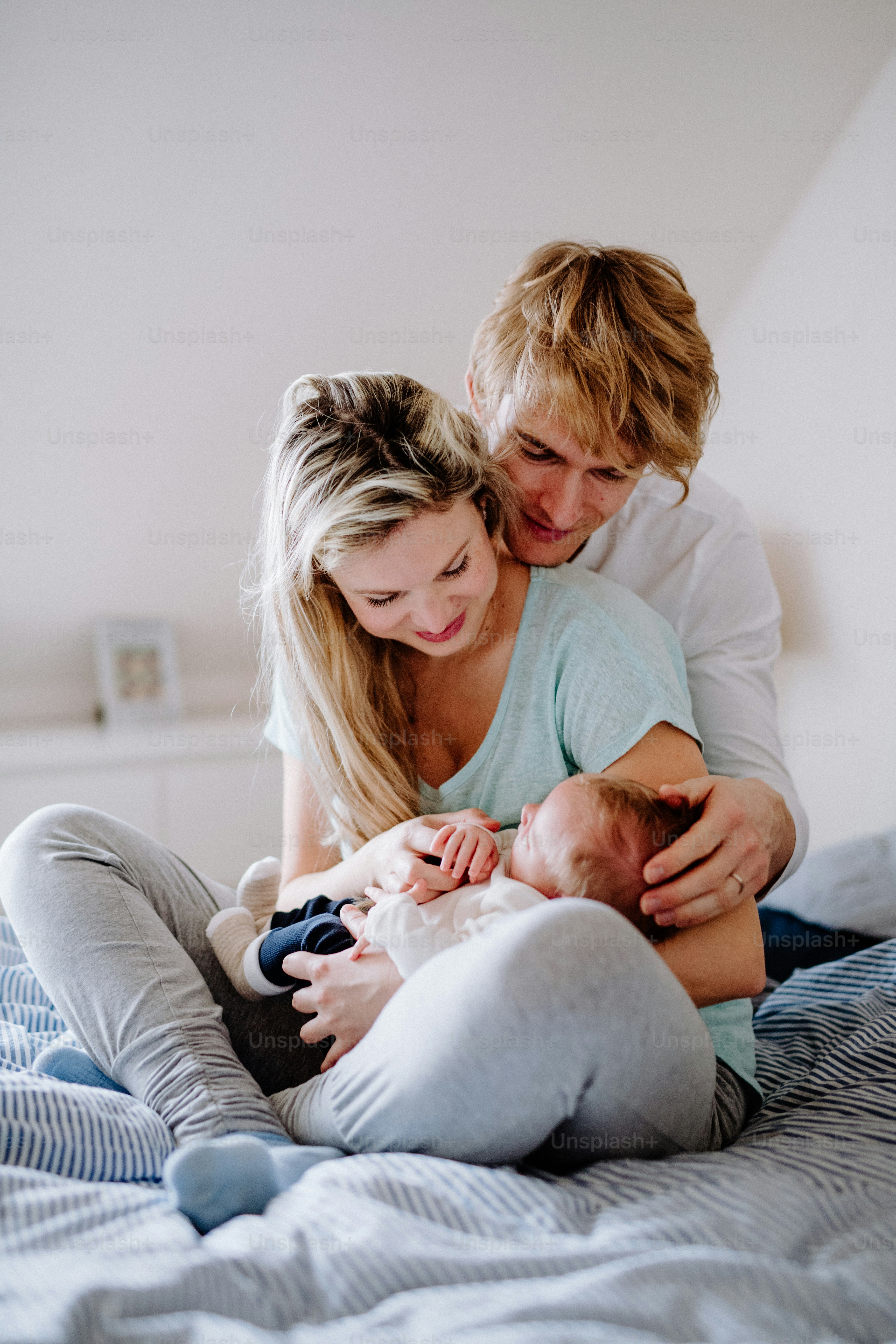 Beautiful young parents holding a newborn baby at home, sitting on bed ...