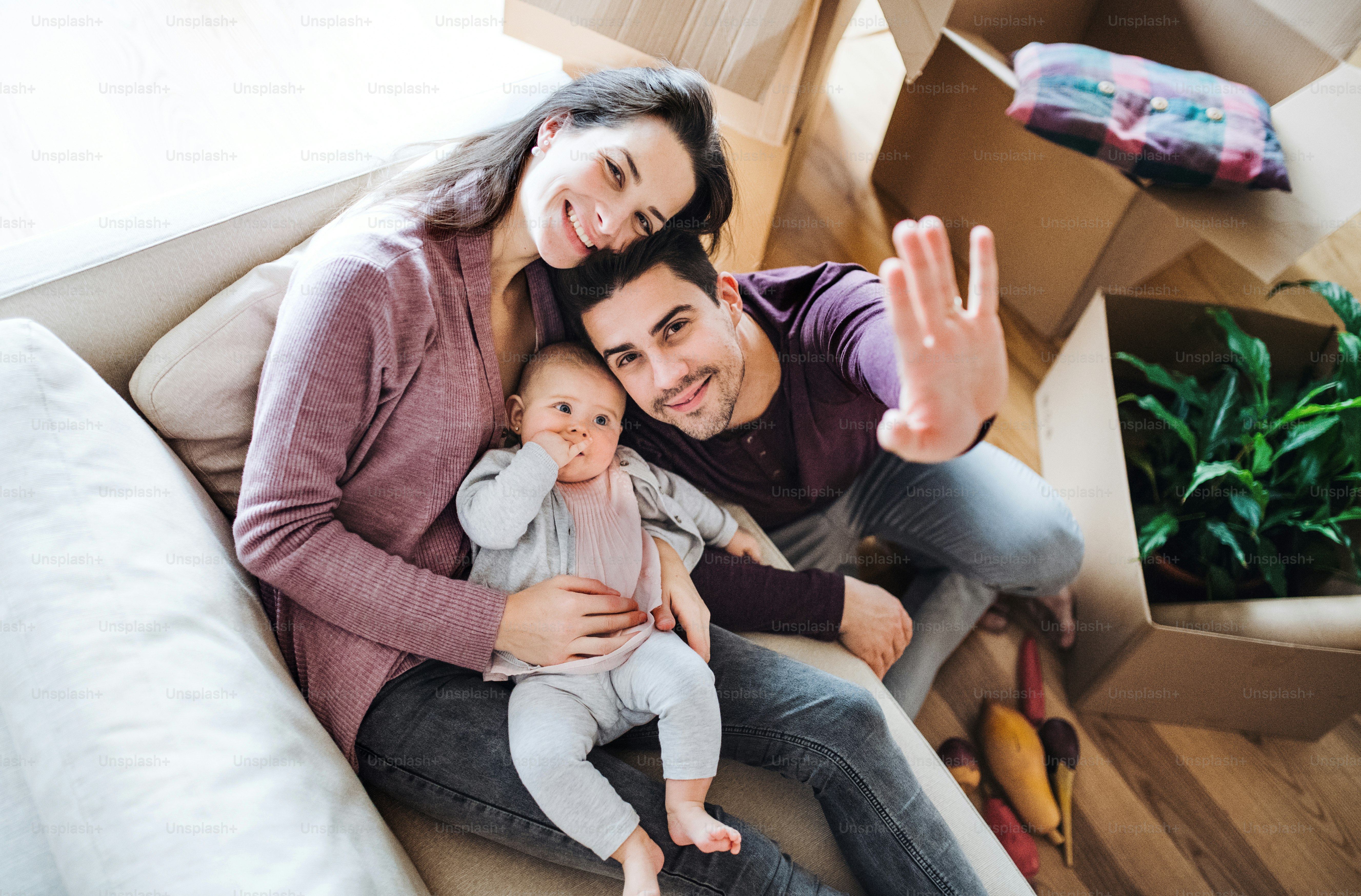 A portrait of happy young couple with a baby and cardboard boxes, moving in a new home. A top ...
