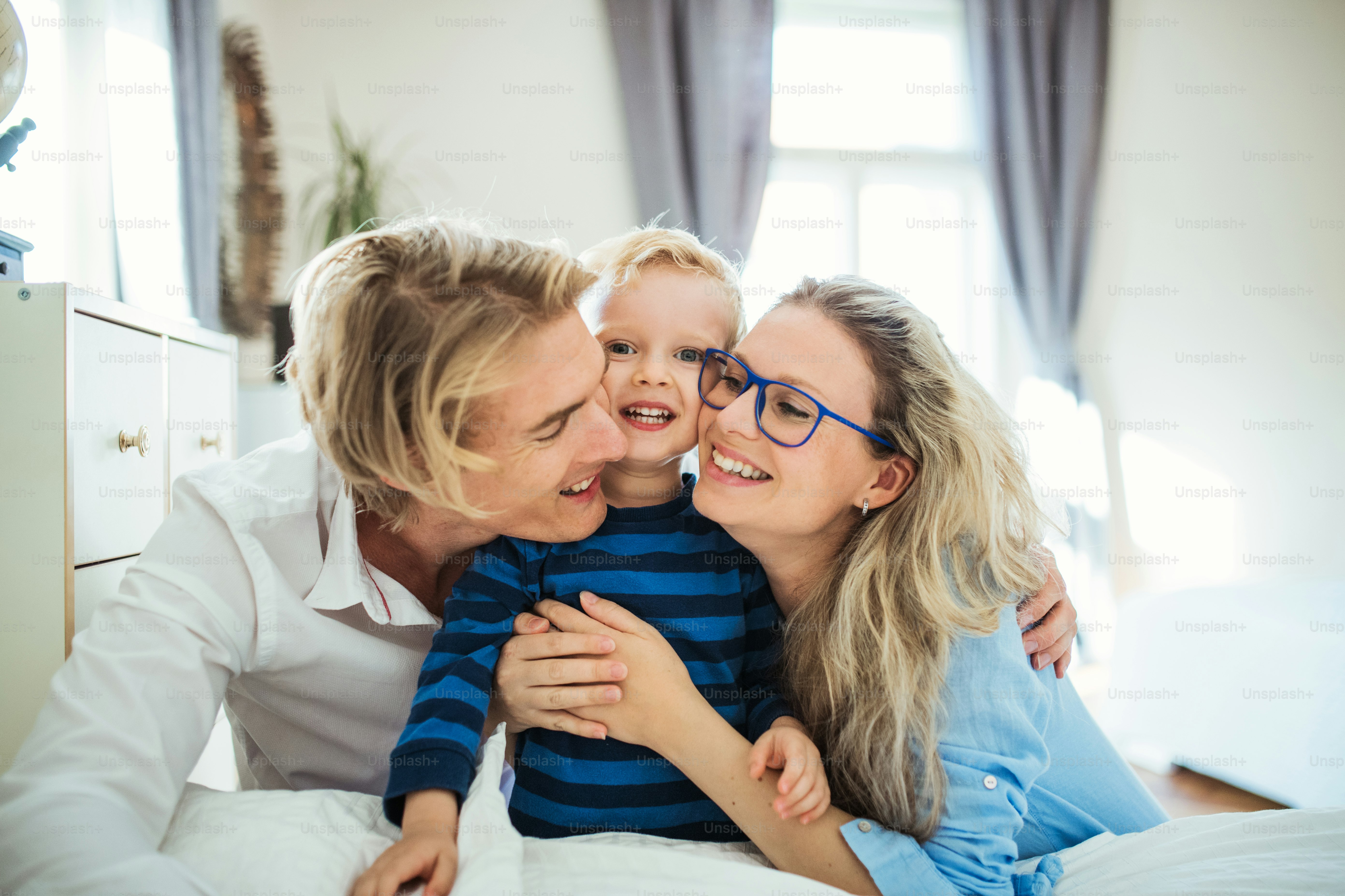 Happy young happy parents hugging their toddler son inside in a bedroom ...