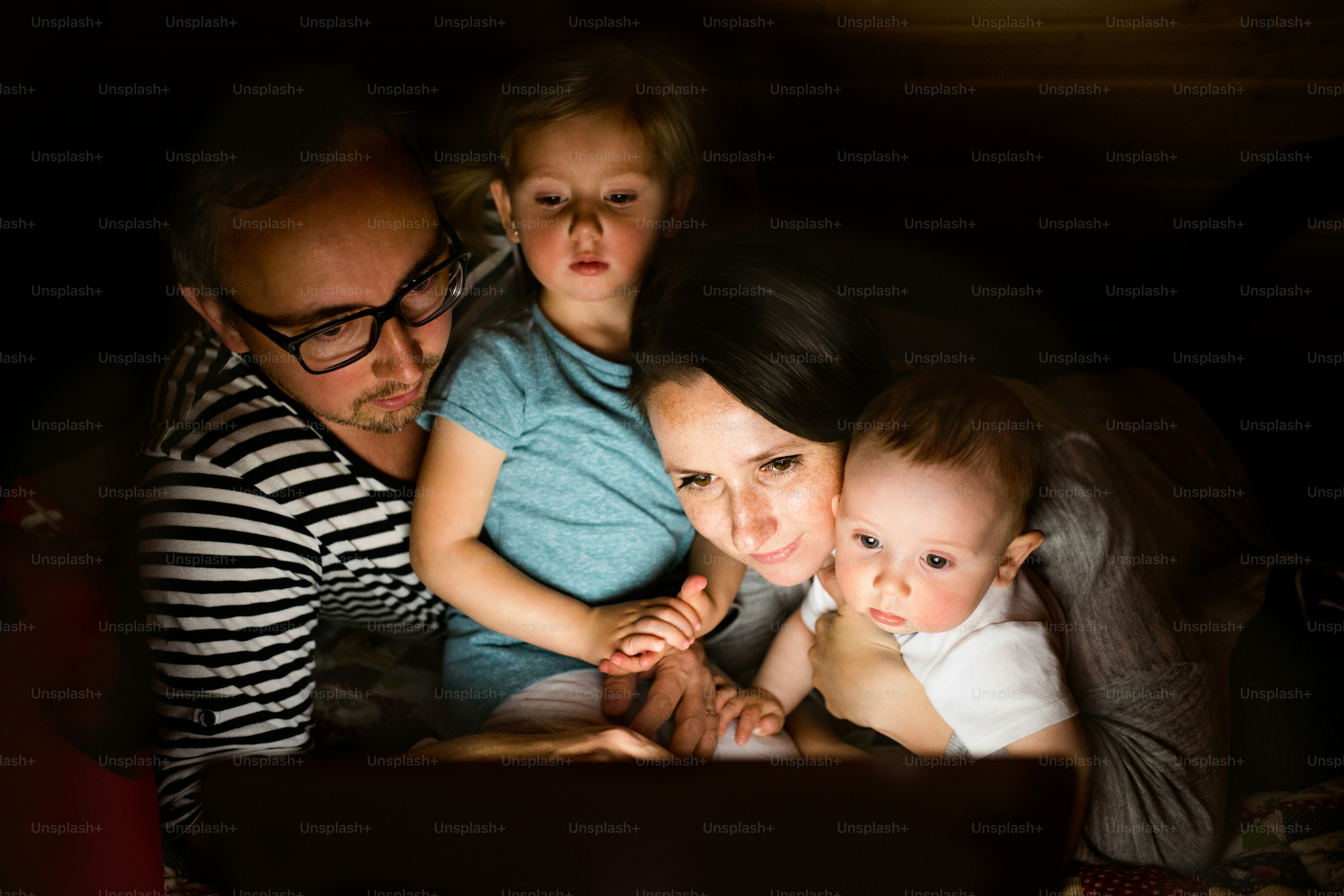 Young parents at home at night with their little children watching ...