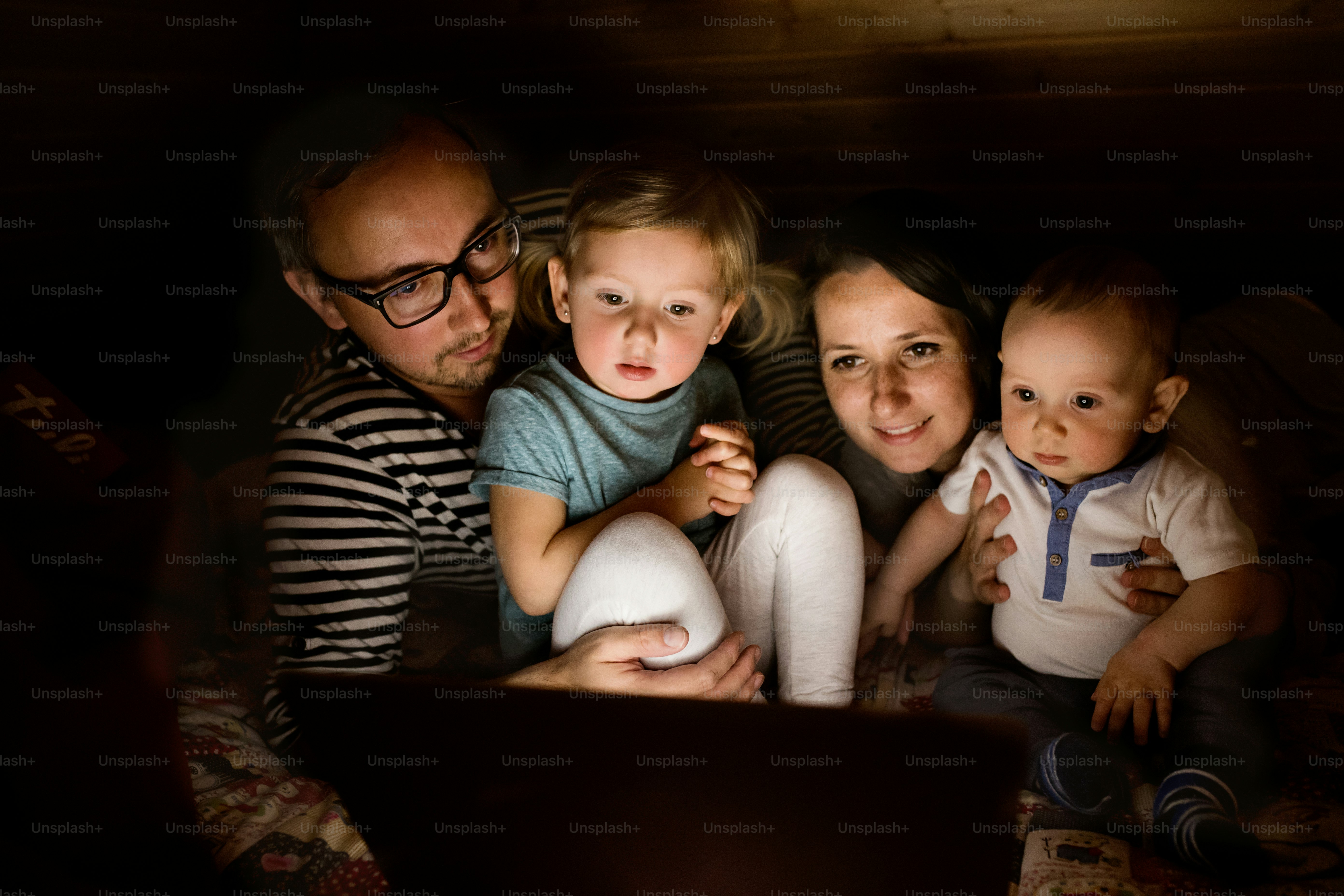 Young parents at home at night with their little children watching ...