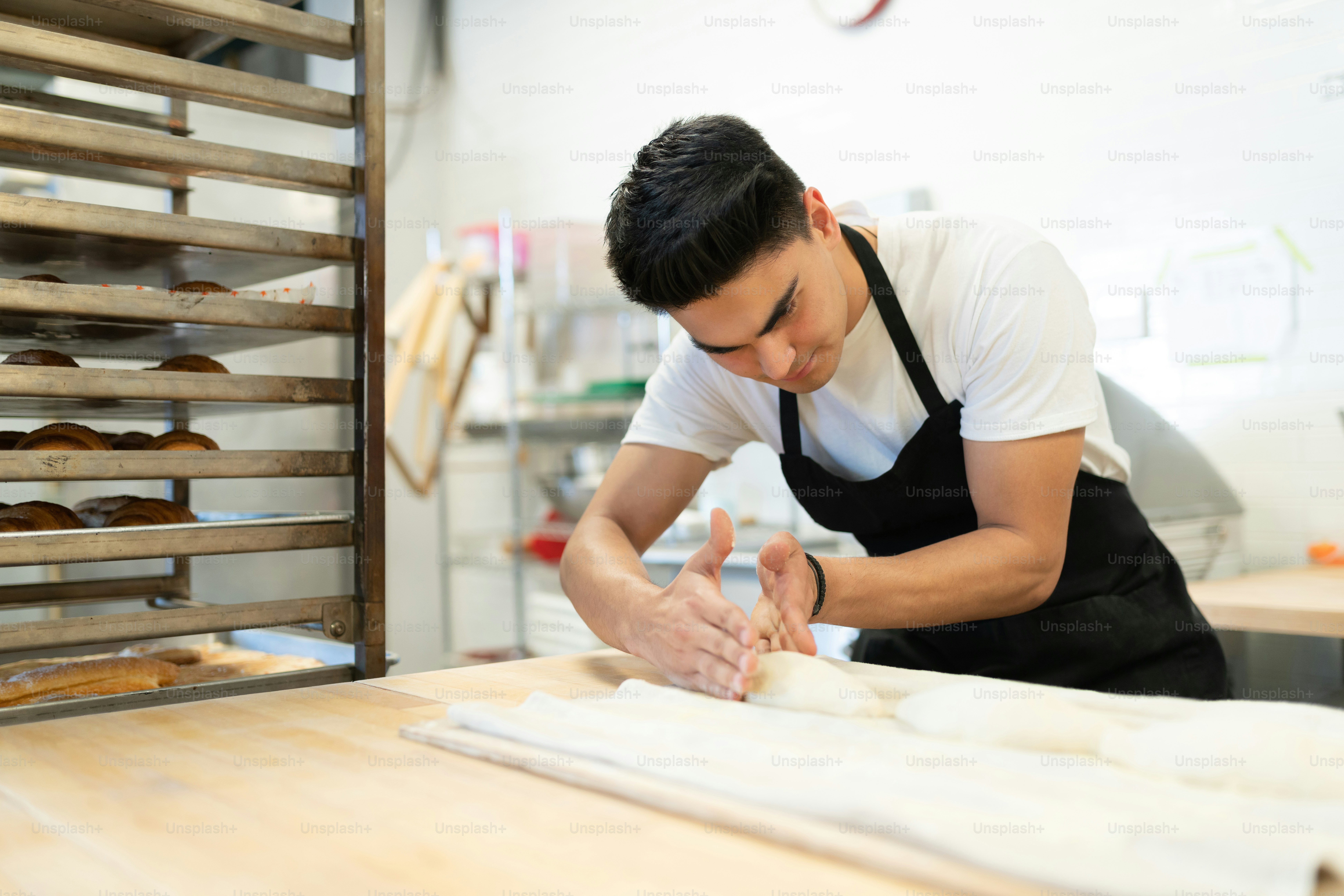 Focused male baker working with dough and making a few loaves of bread ...