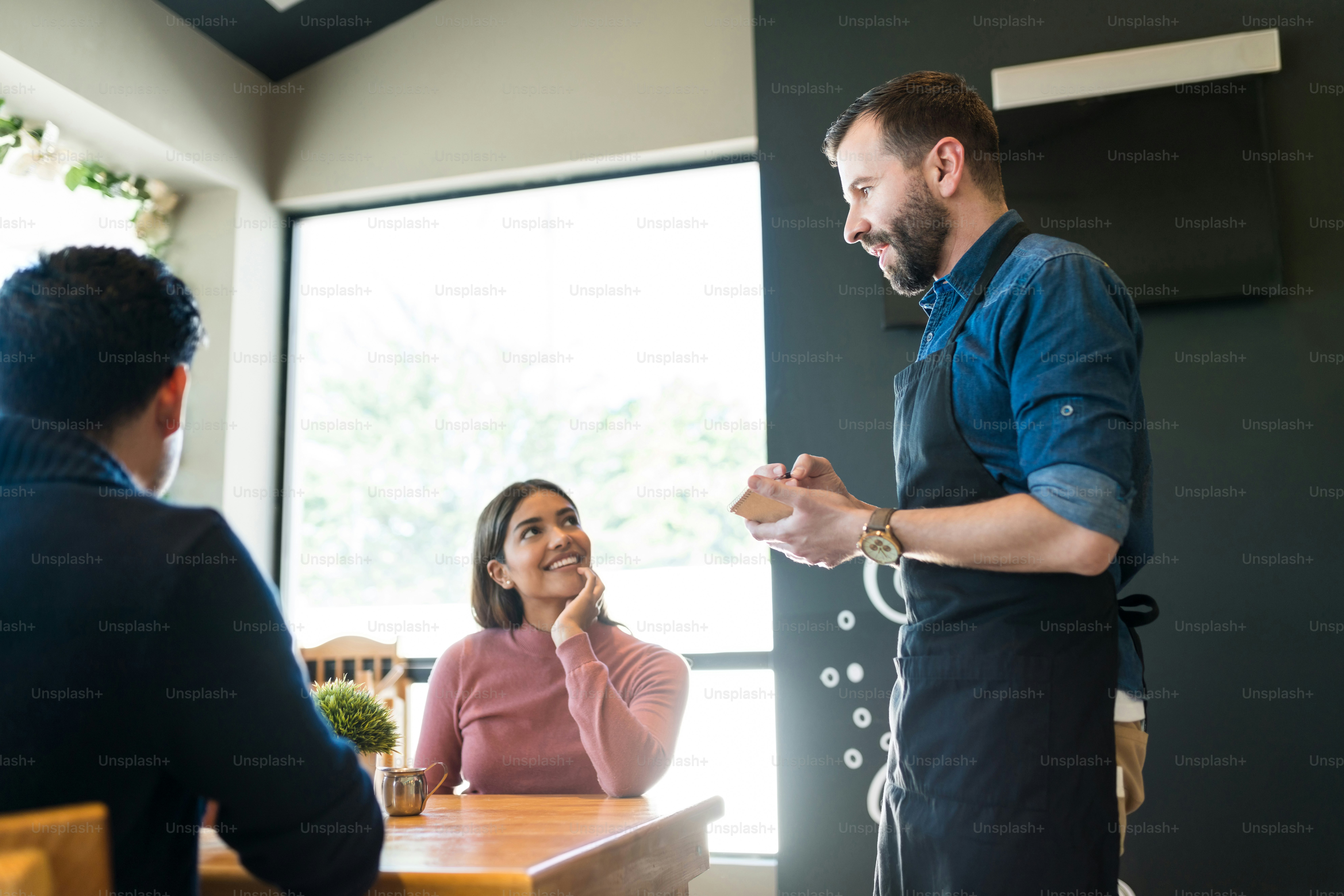 Mid adult waiter taking orders from smiling customers in restaurant ...