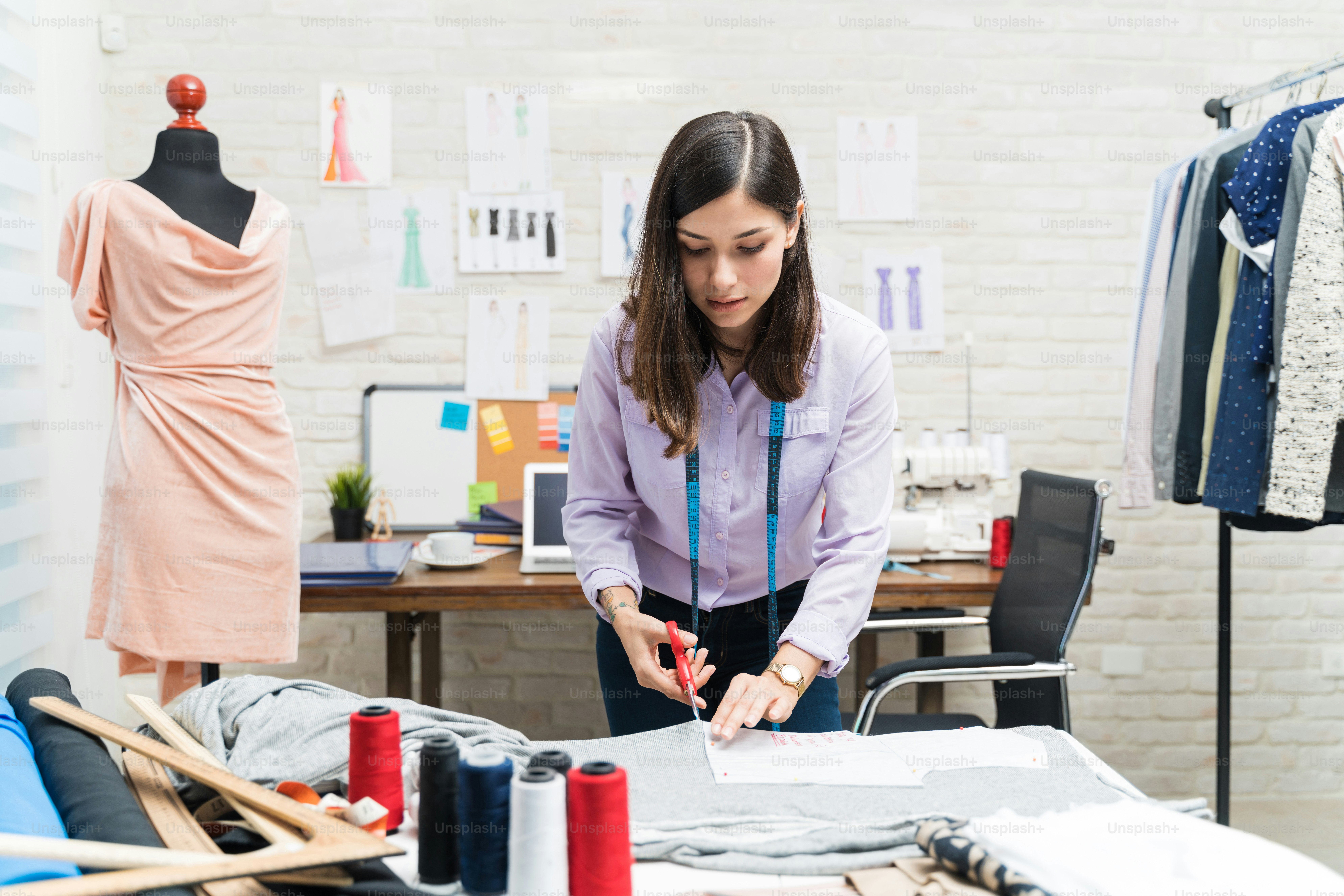 Confident female tailor cutting fabric with scissors on workbench at ...
