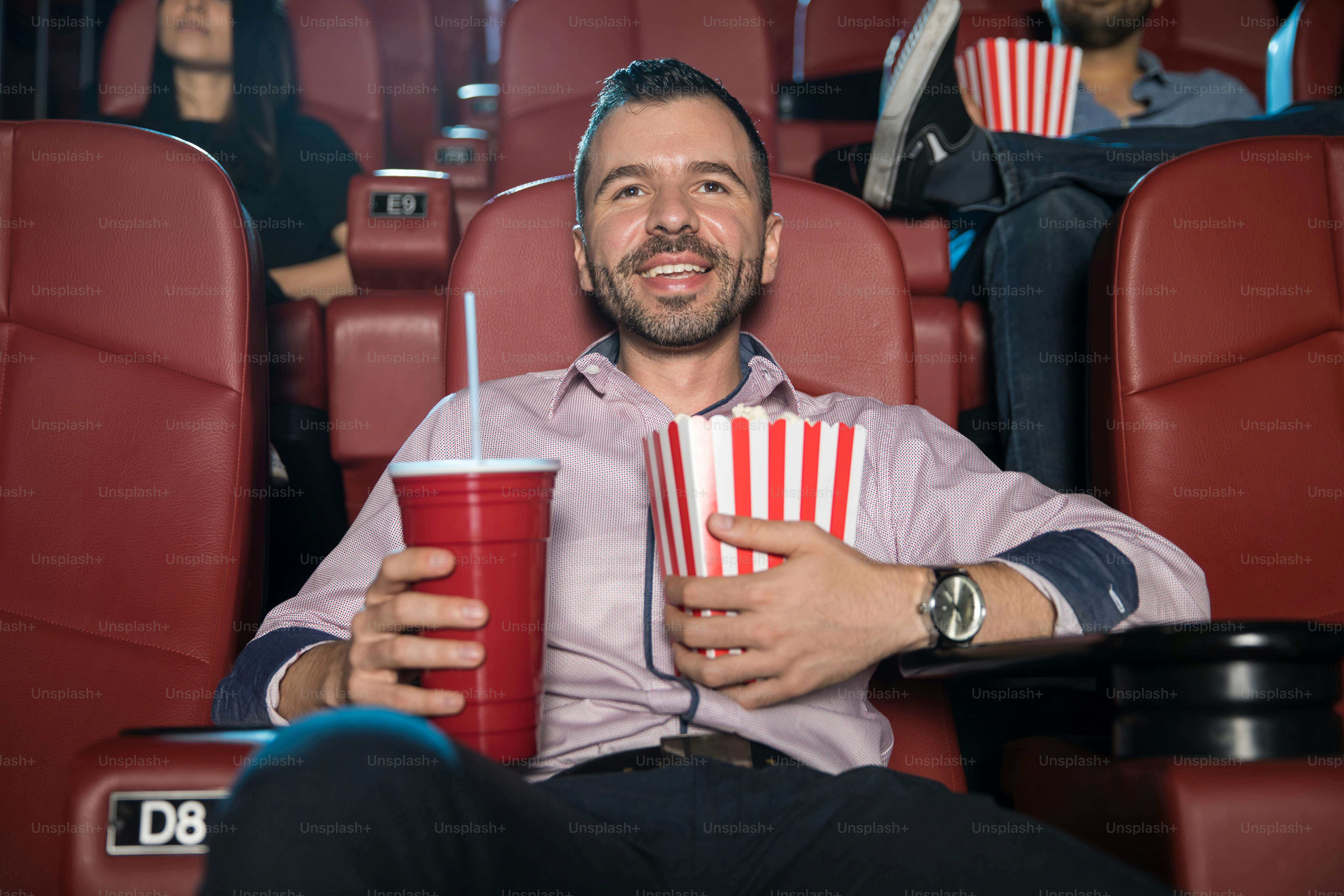 Happy young man with a beard hugging a combo of soda and popcorn while ...