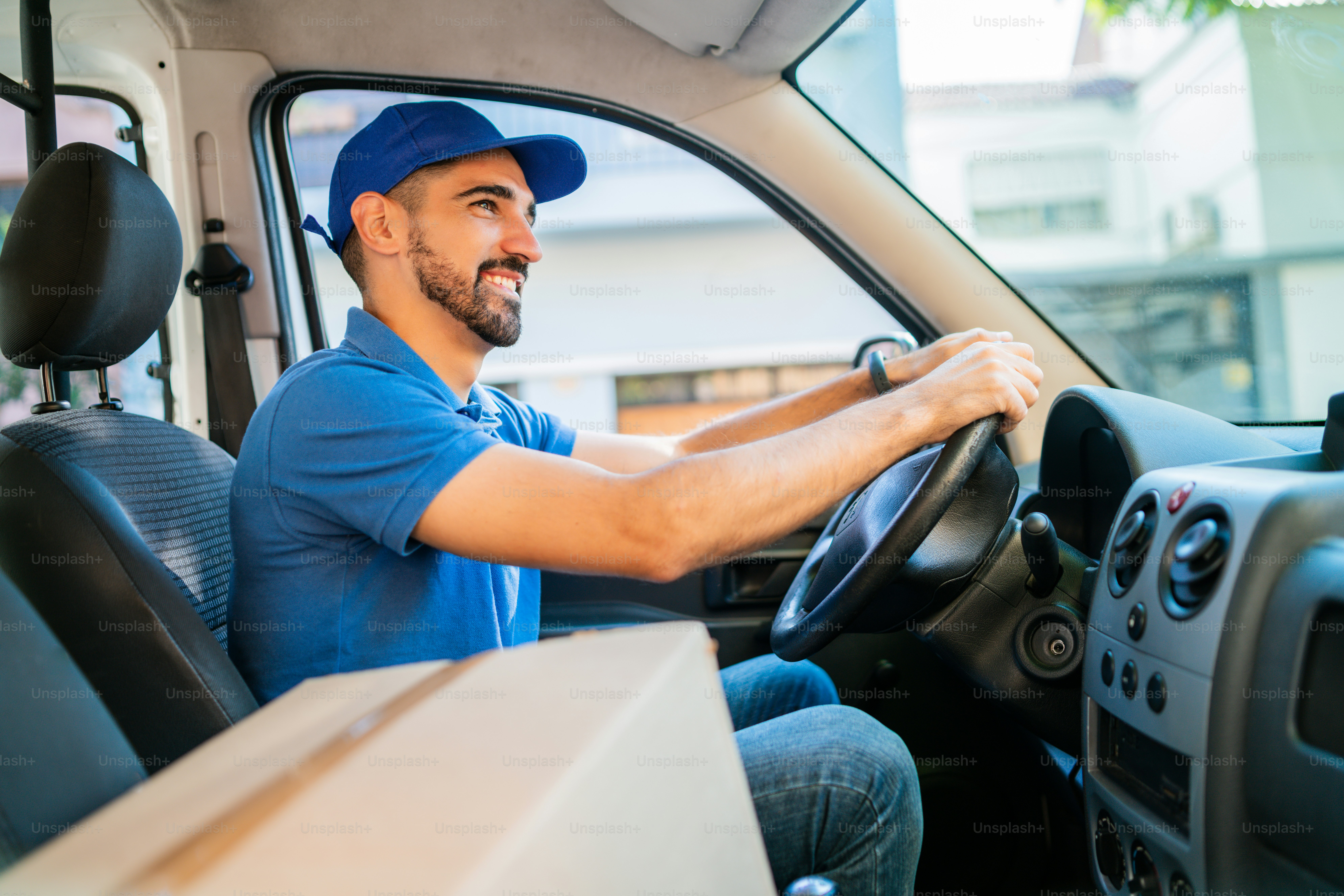 Portrait of a delivery man driver driving van with cardboard boxes on ...