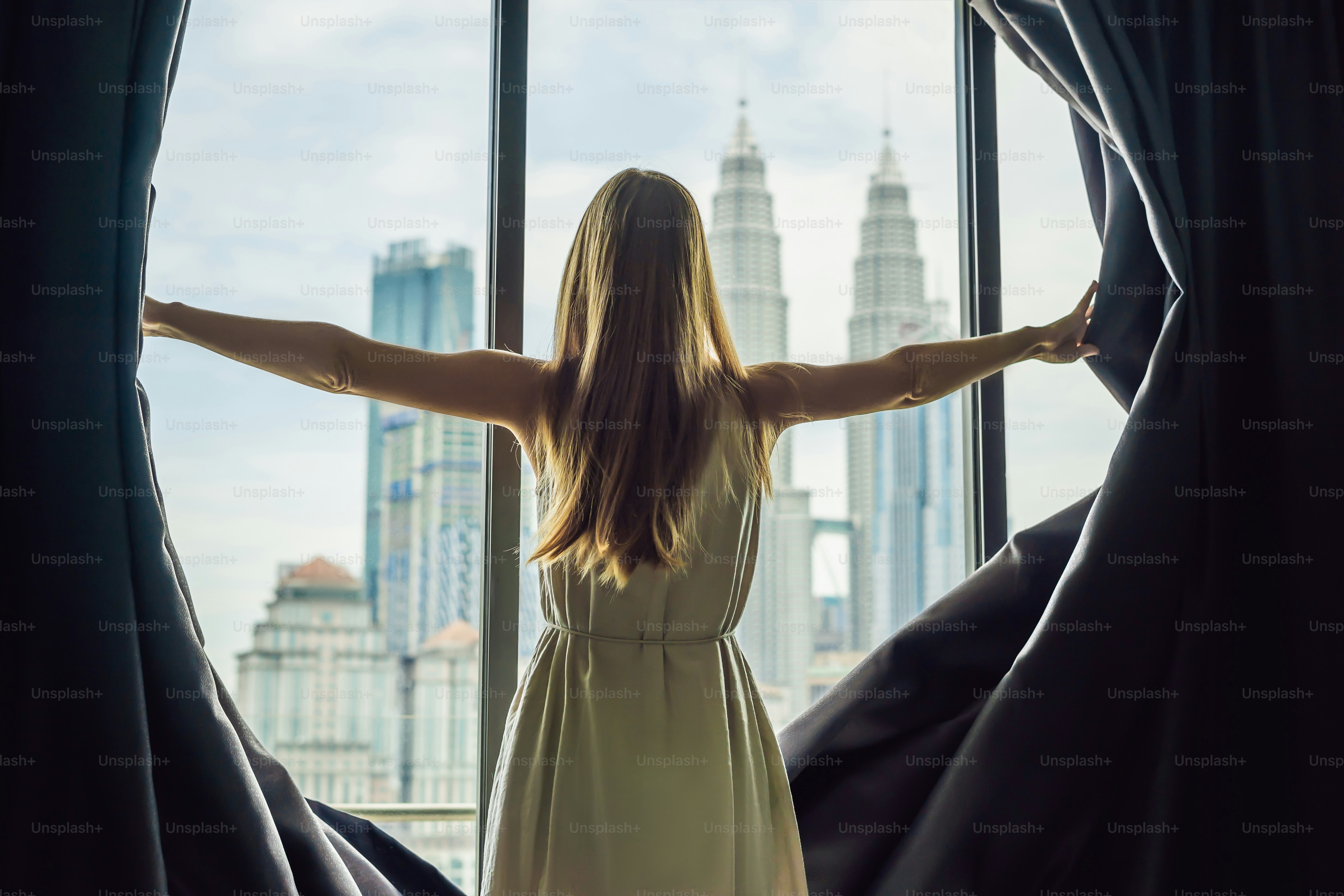 Young woman opens the window curtains and looks at the skyscrapers in ...
