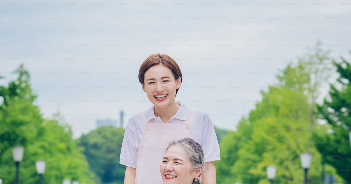 휠체어를 탄 여성과 앞치마를 두른 젊은 여성이 야외를 돌보고 있다 사진 Unsplash의 행복 이미지