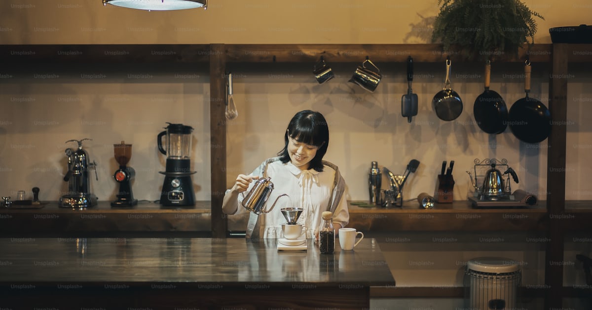 차분한 조명이 켜진 공간에서 손을 뚝뚝 떨어뜨리며 커피를 끓이는 젊은 여성 사진 Unsplash의 한 명의 여성만 이미지