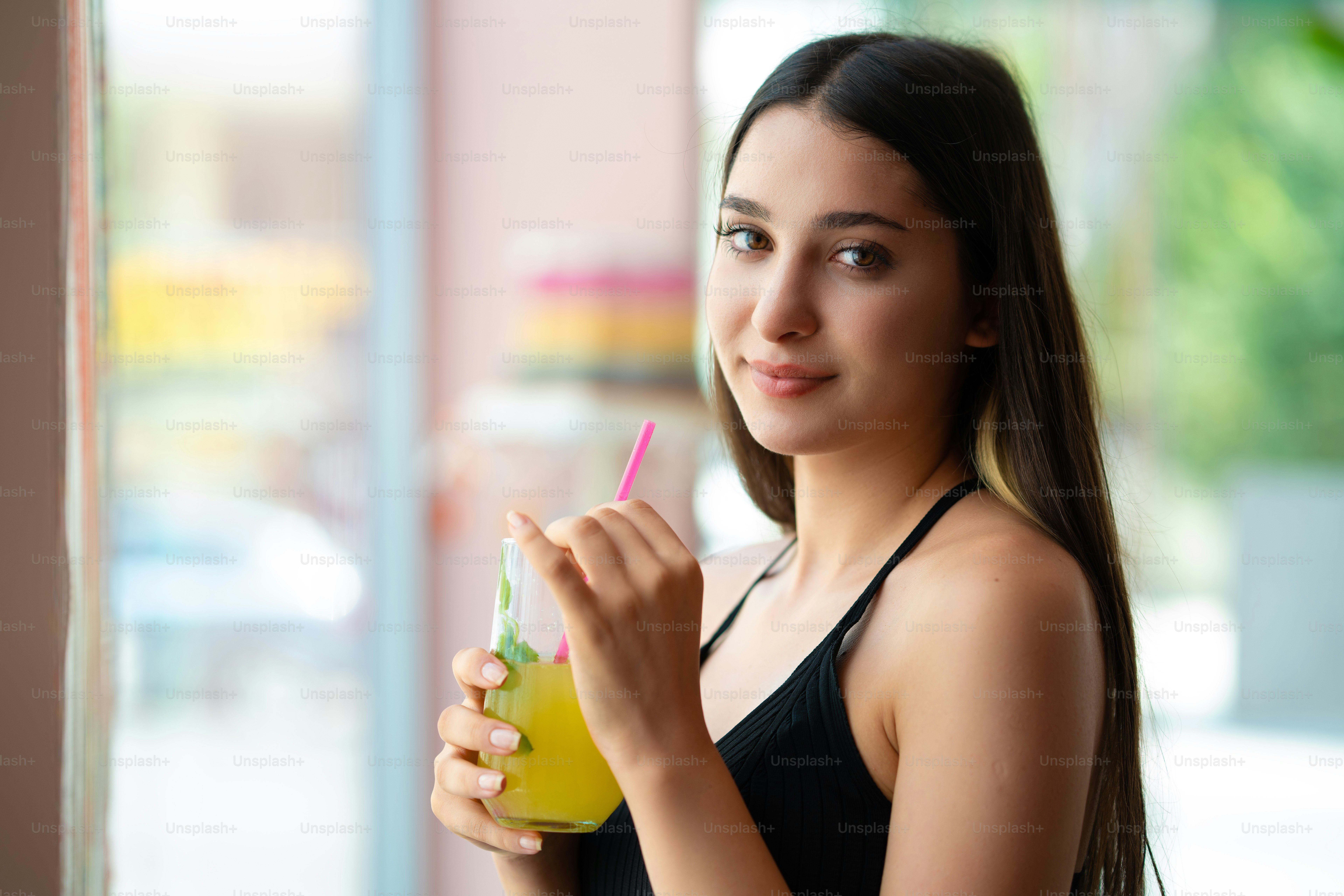 Young woman smiling and drinking some beverage in front of window. High ...