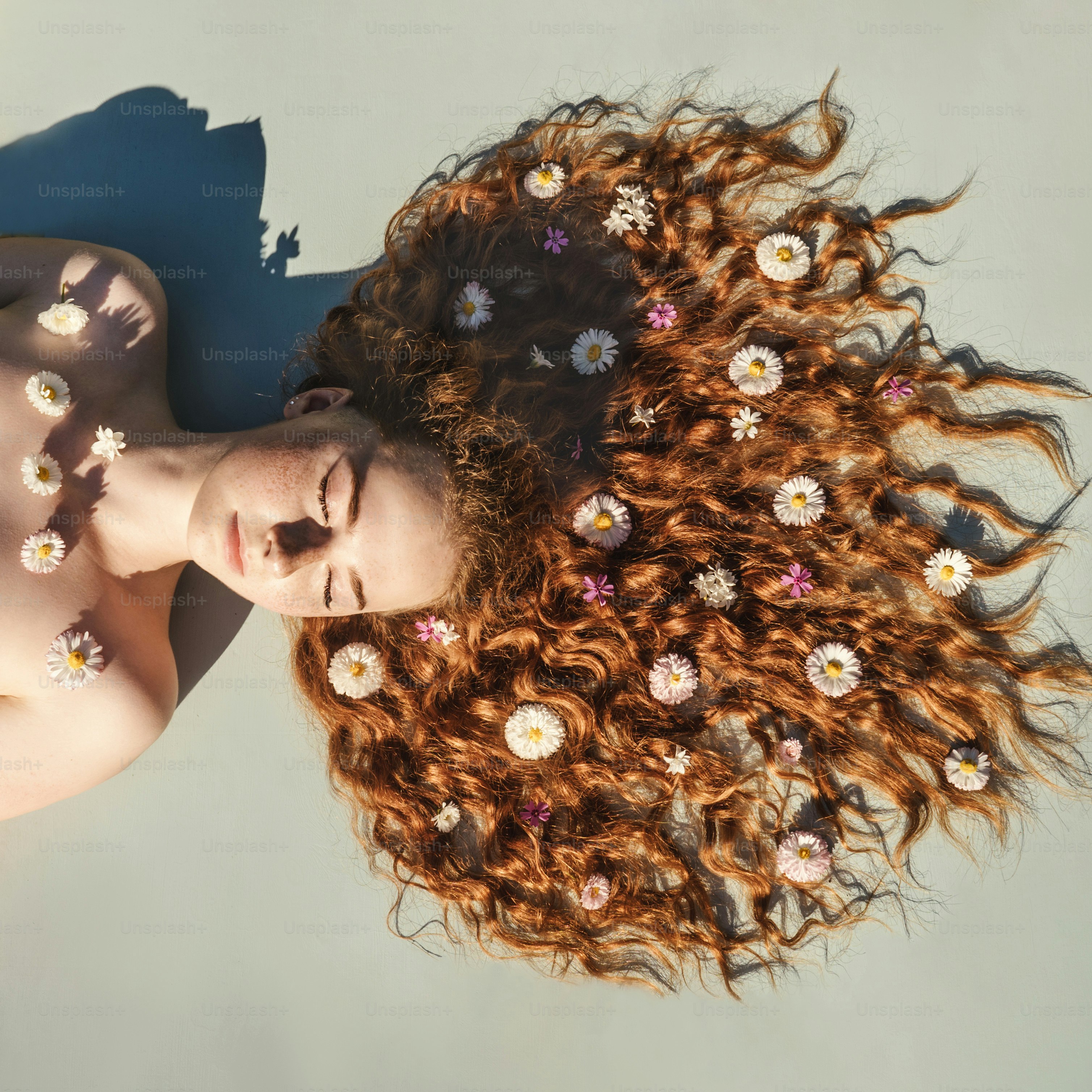 Close up portrait of young ginger curly girl with flowers in hair above ...