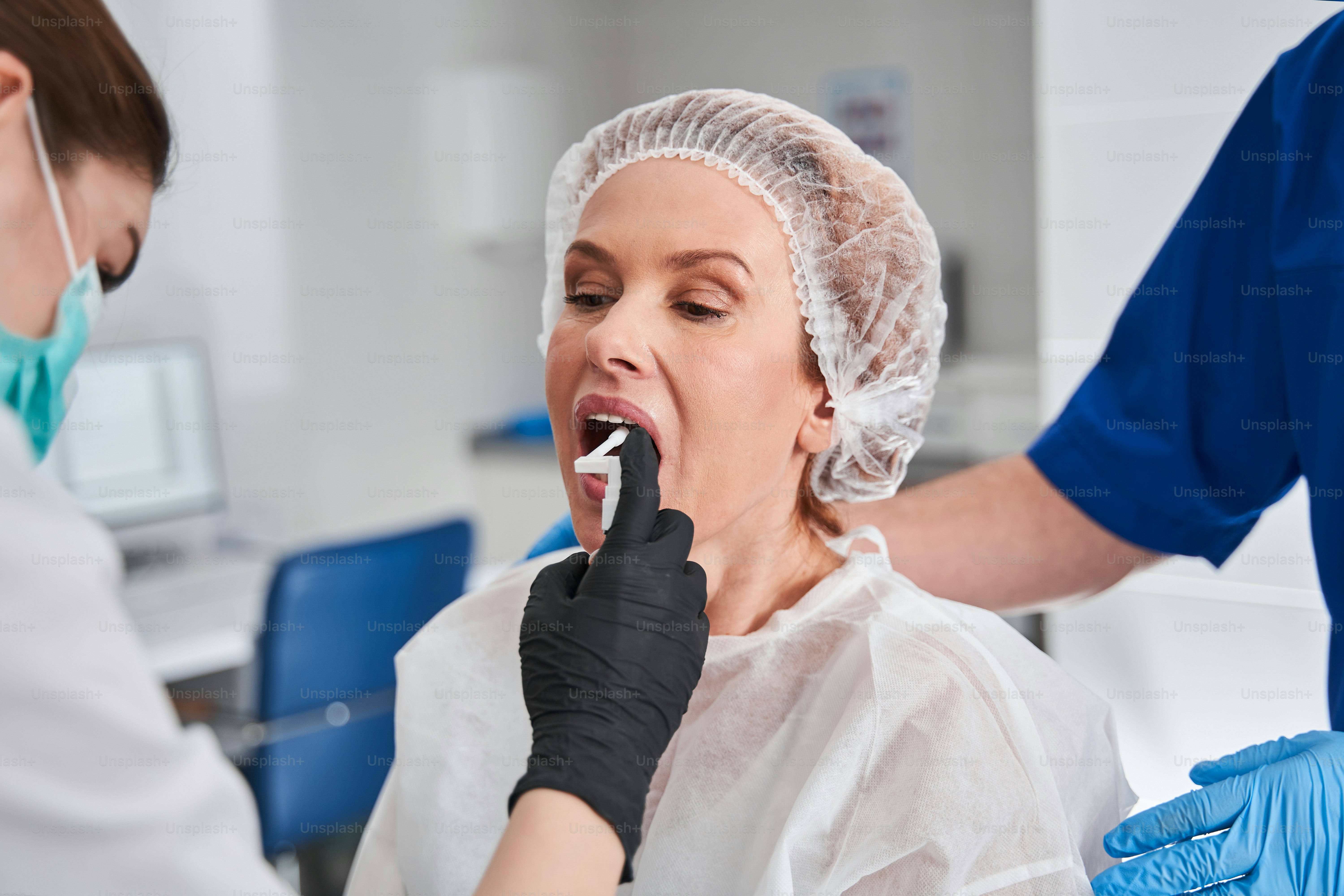 Attentive nurse spraying anaesthesia at the female patient mouth before ...