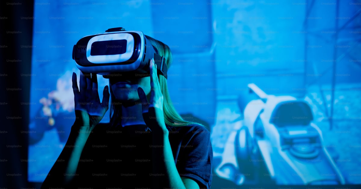 Vr 헤드셋을 착용한 새로운 미래형 비디오 게임의 젊은 개발자가 프레젠테이션 중 가상 머신이 있는 대형 스크린에 서 있다 사진