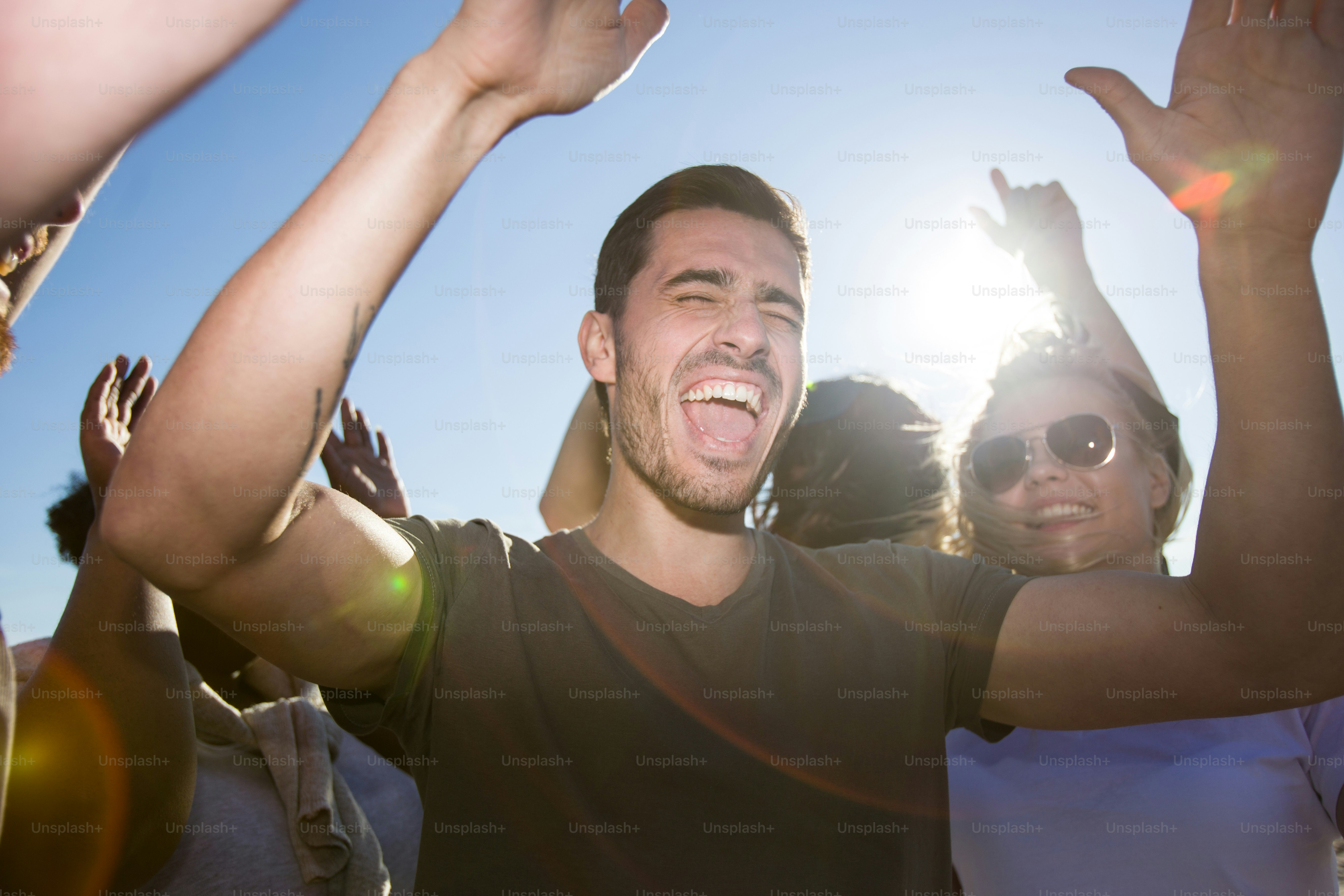 Ecstatic guy laughing while deancing among his friends on sunny day ...