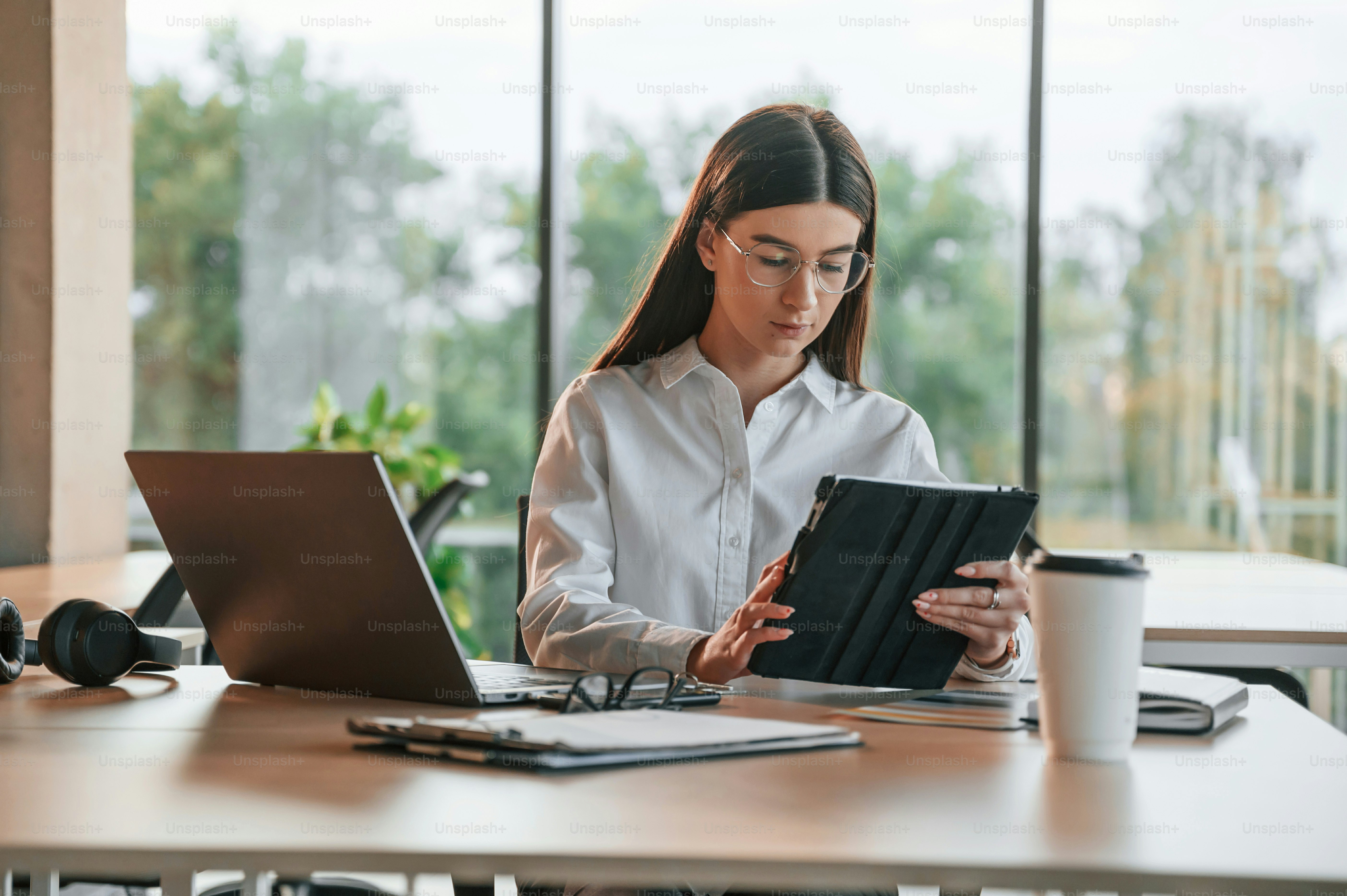 Using tablet. Beautiful young woman in white clothes is working in ...