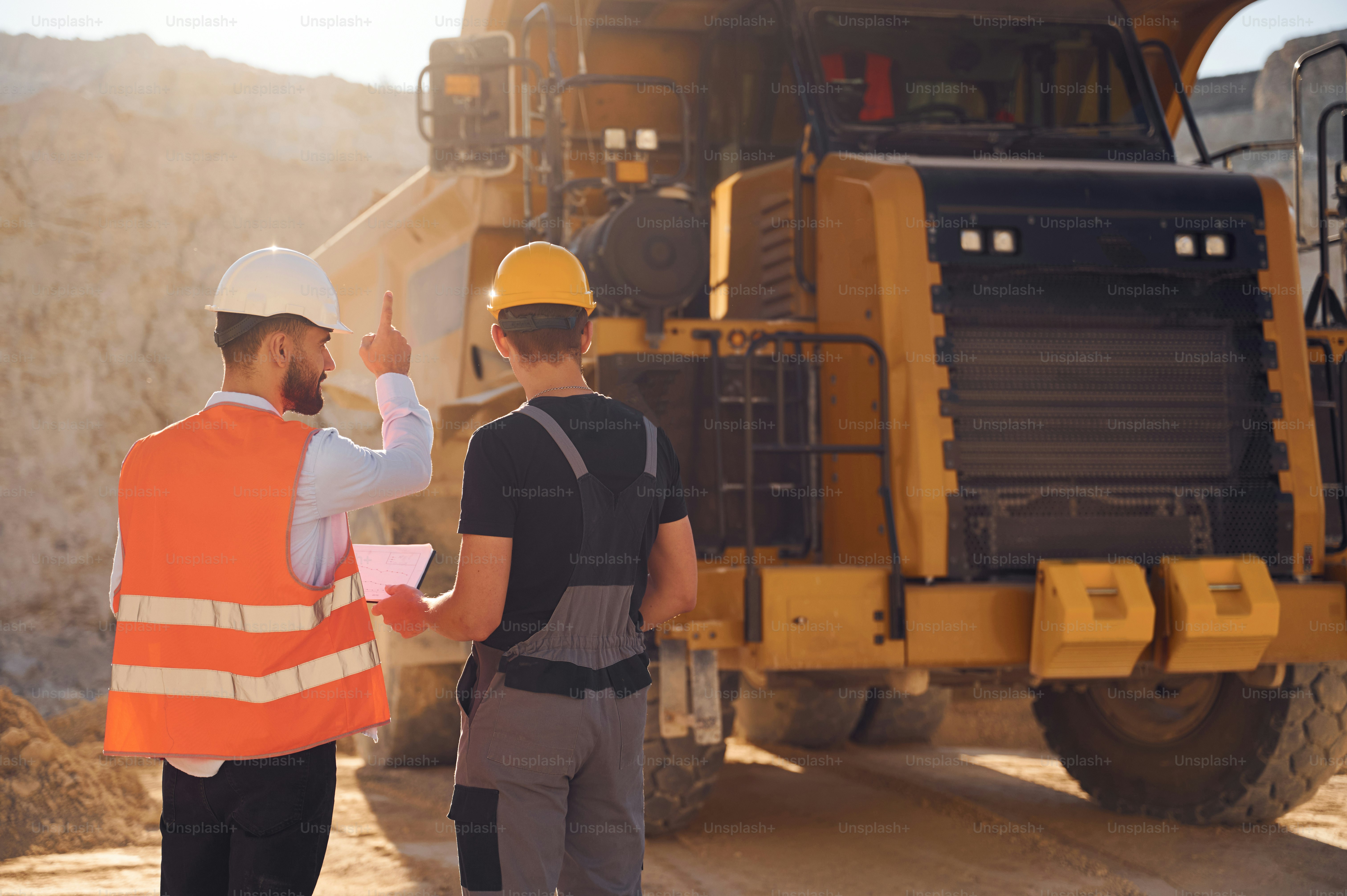 Looking at big haul truck. Two men in uniform are working together in ...