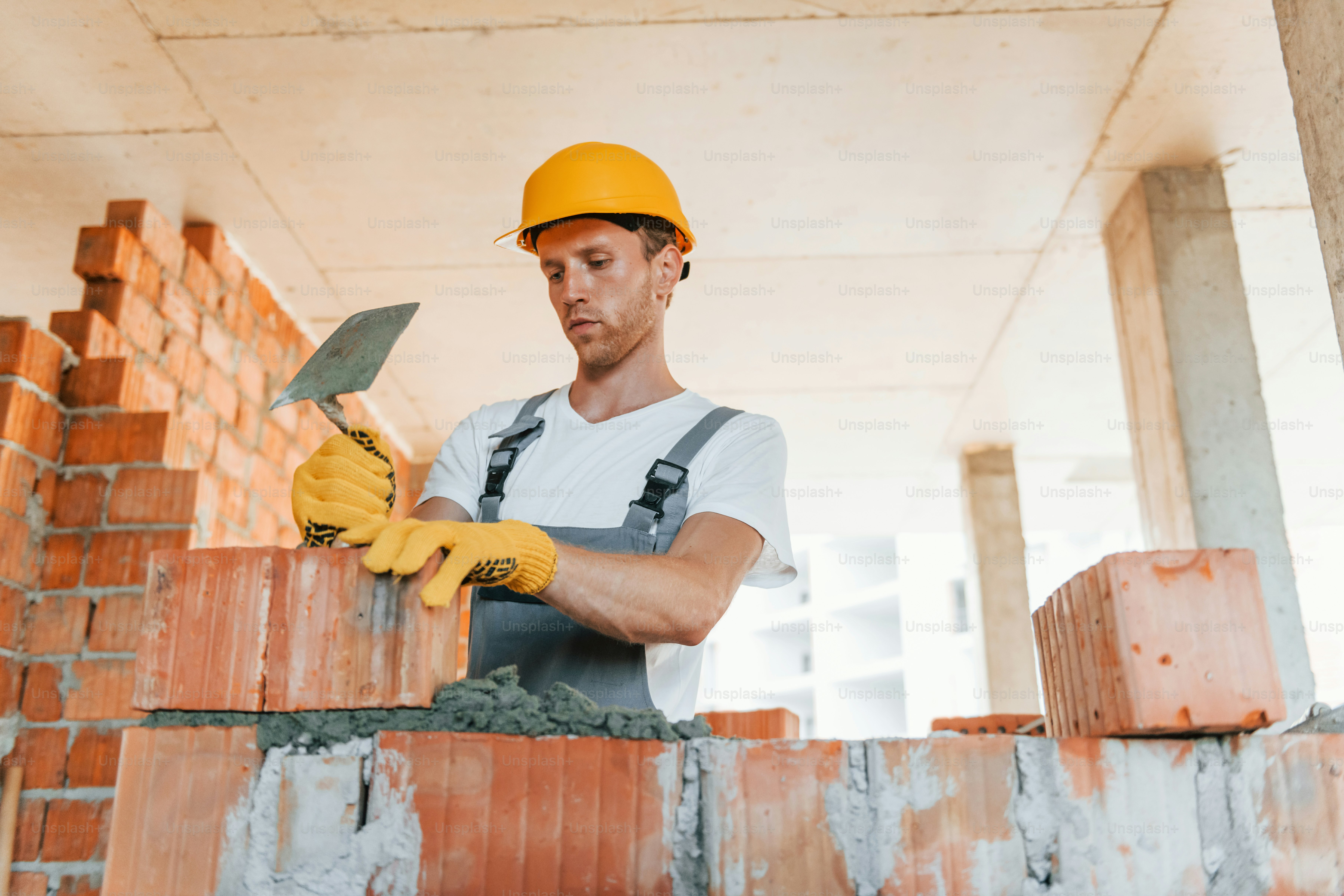 Working by using bricks. Young man in uniform at construction at ...