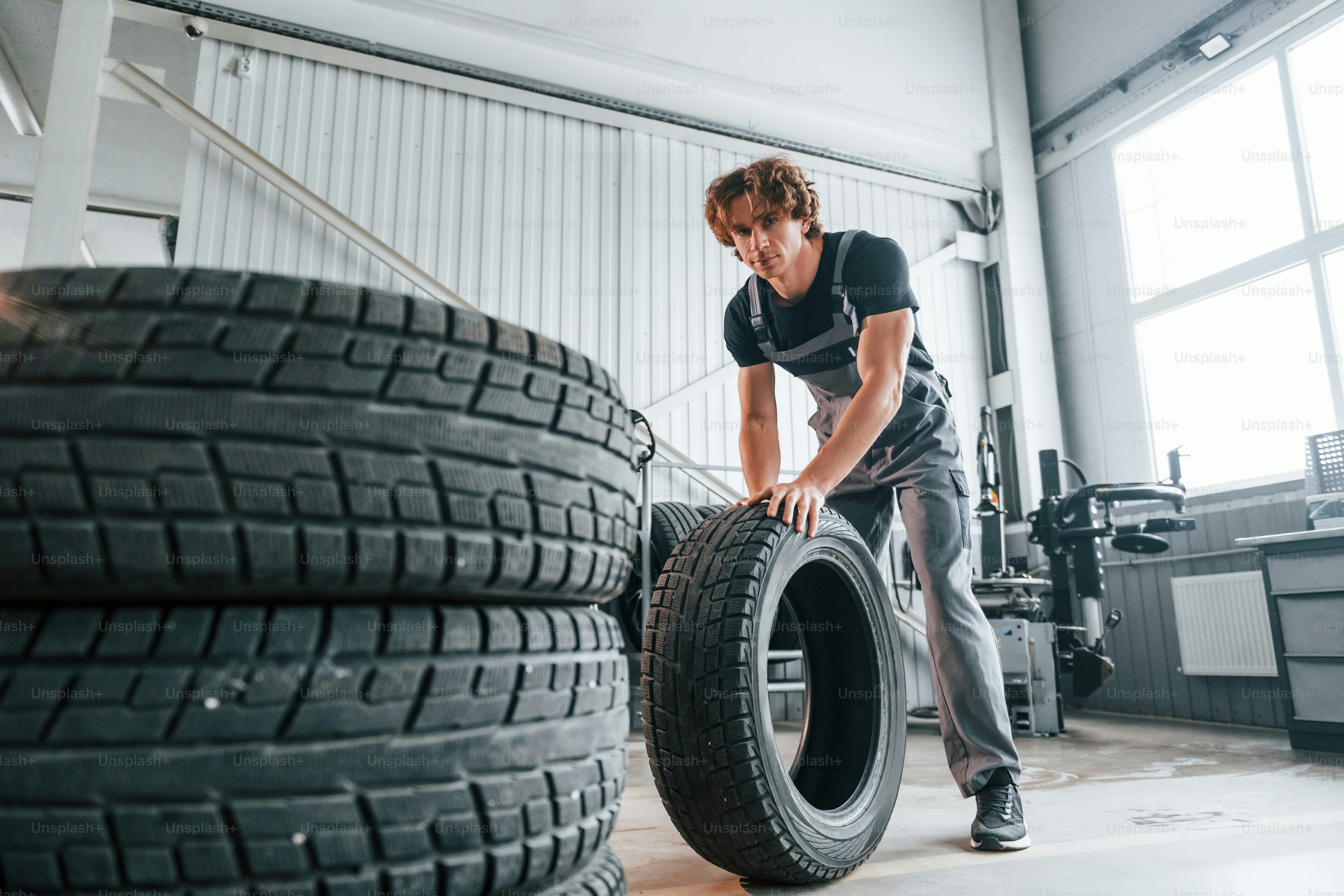 Rolls the tire. Adult man in grey colored uniform works in the ...