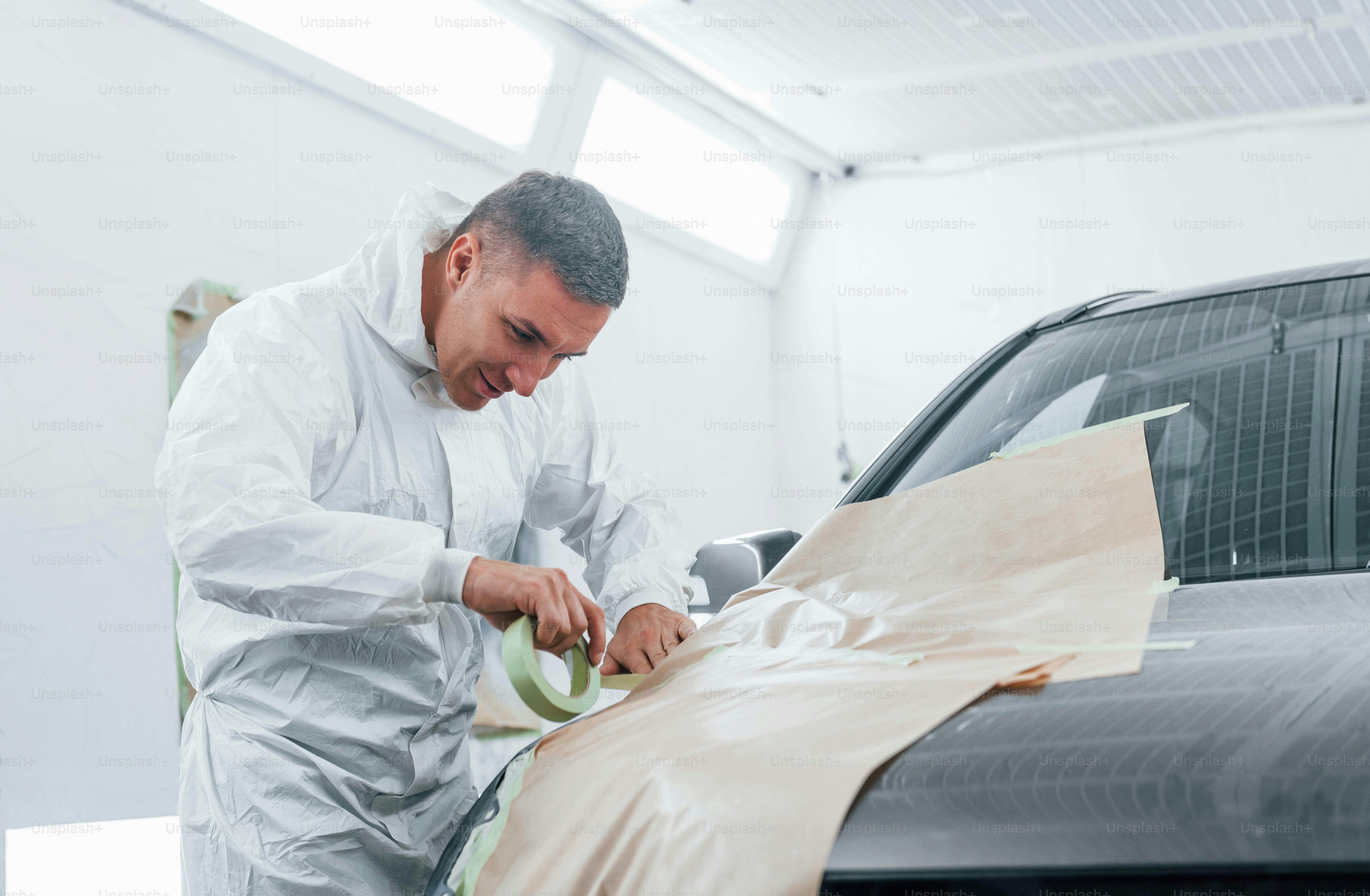Covering car by brown cloth. Caucasian automobile repairman in uniform ...