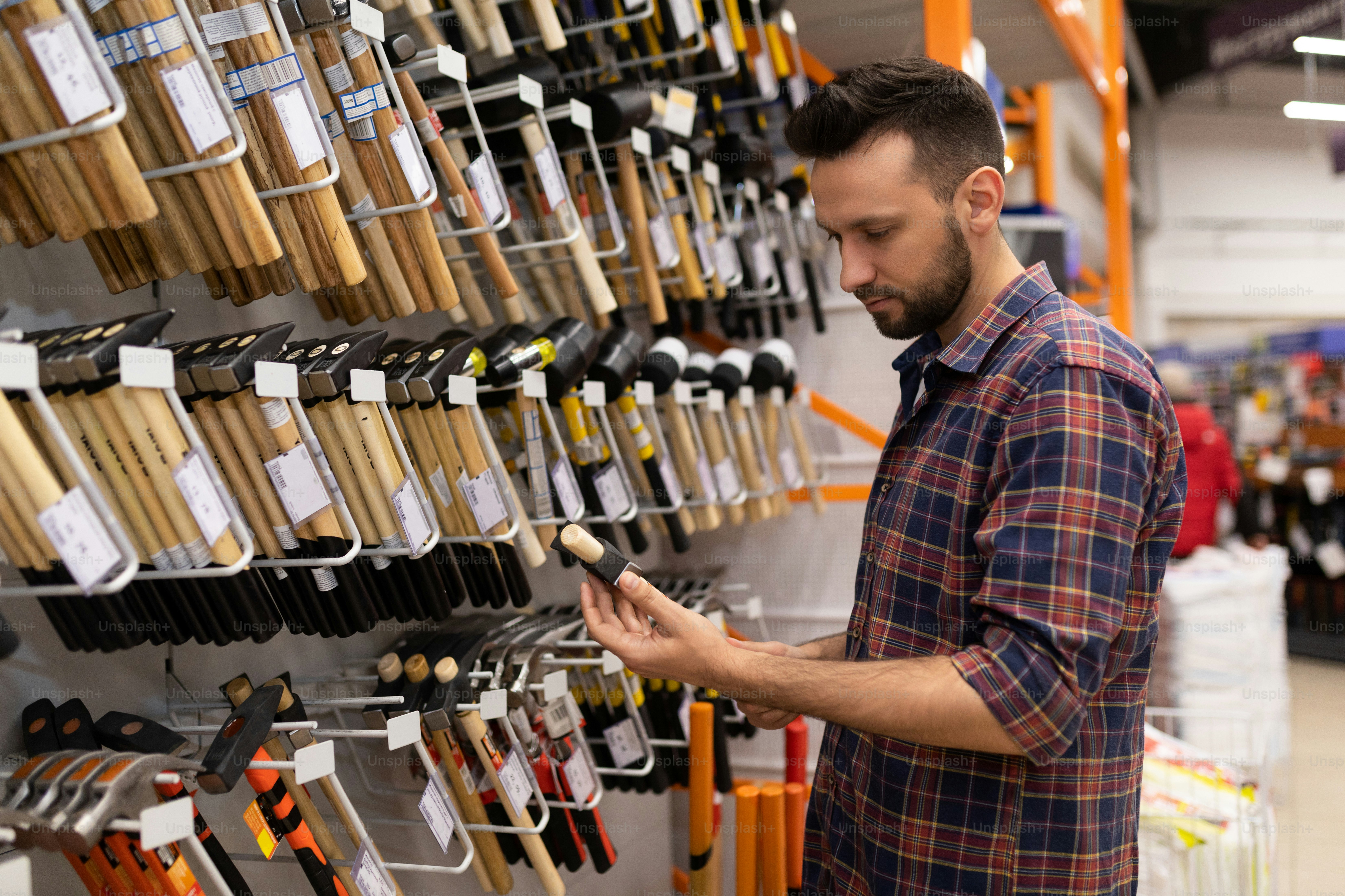A man in a hardware store picks a hammer next to a display case with ...