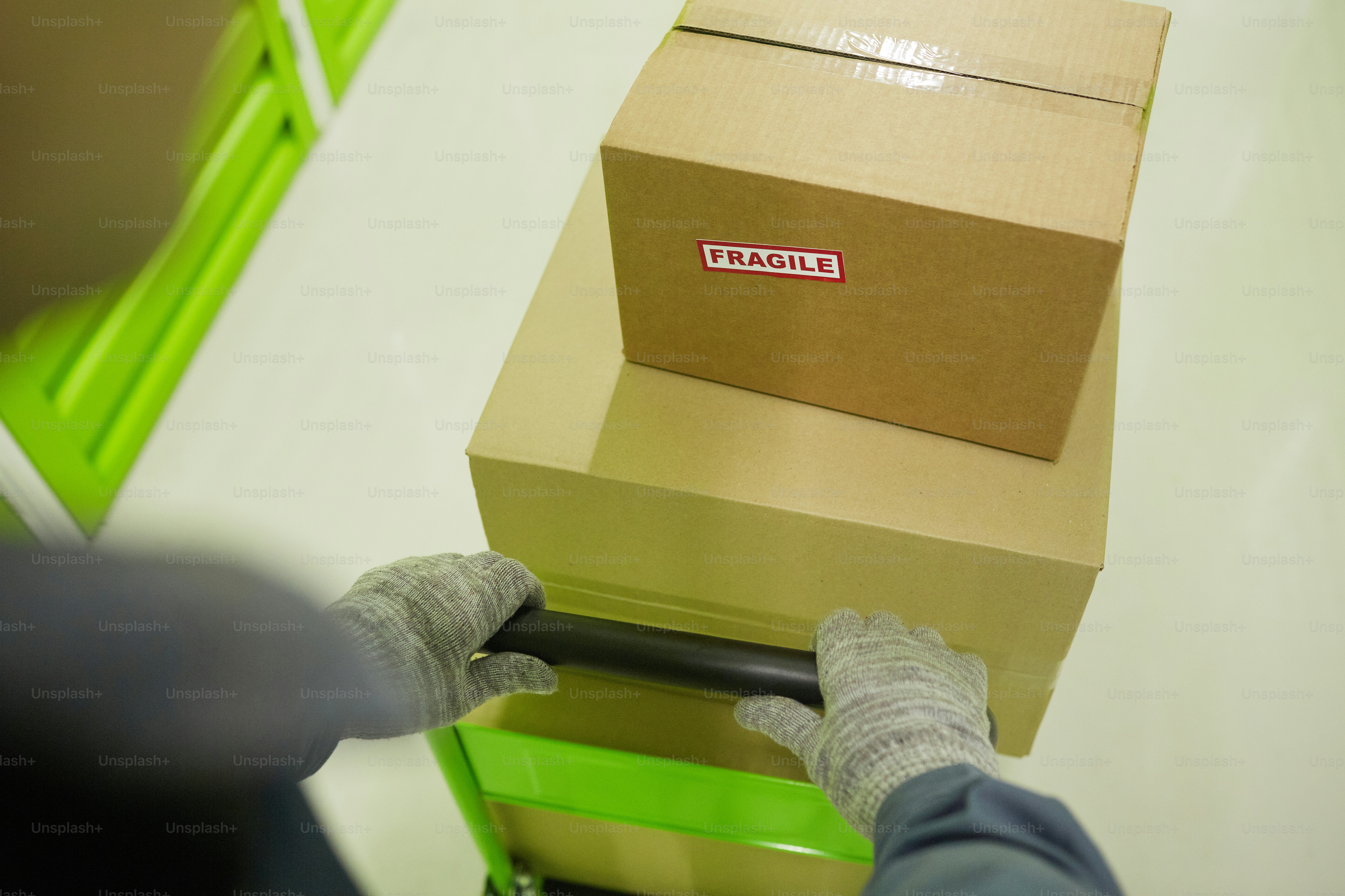 Close-up of person in gloves carrying trolley with cardboard boxes ...