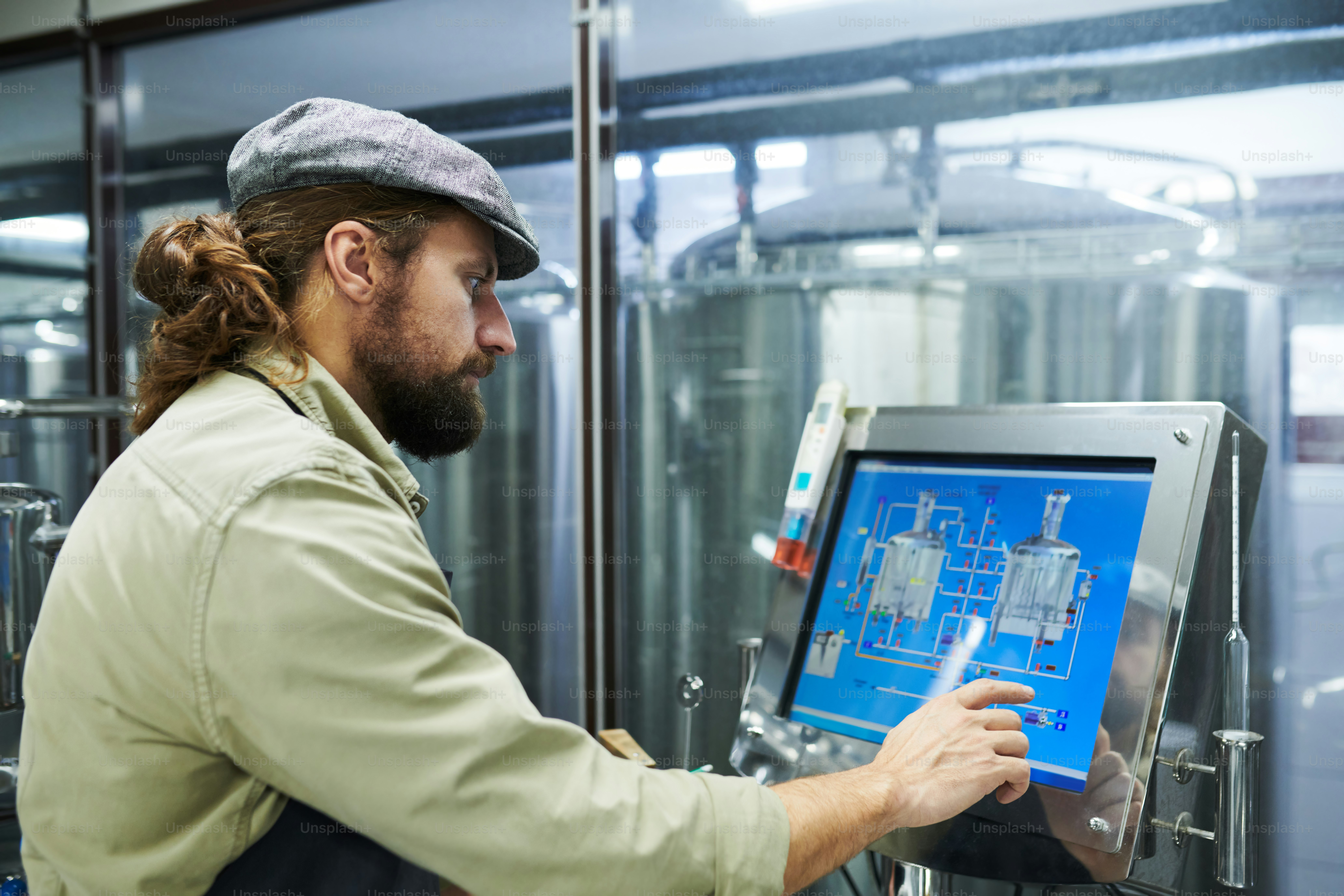 Brewery worker checking scheme on screen when setting brewery equipment ...