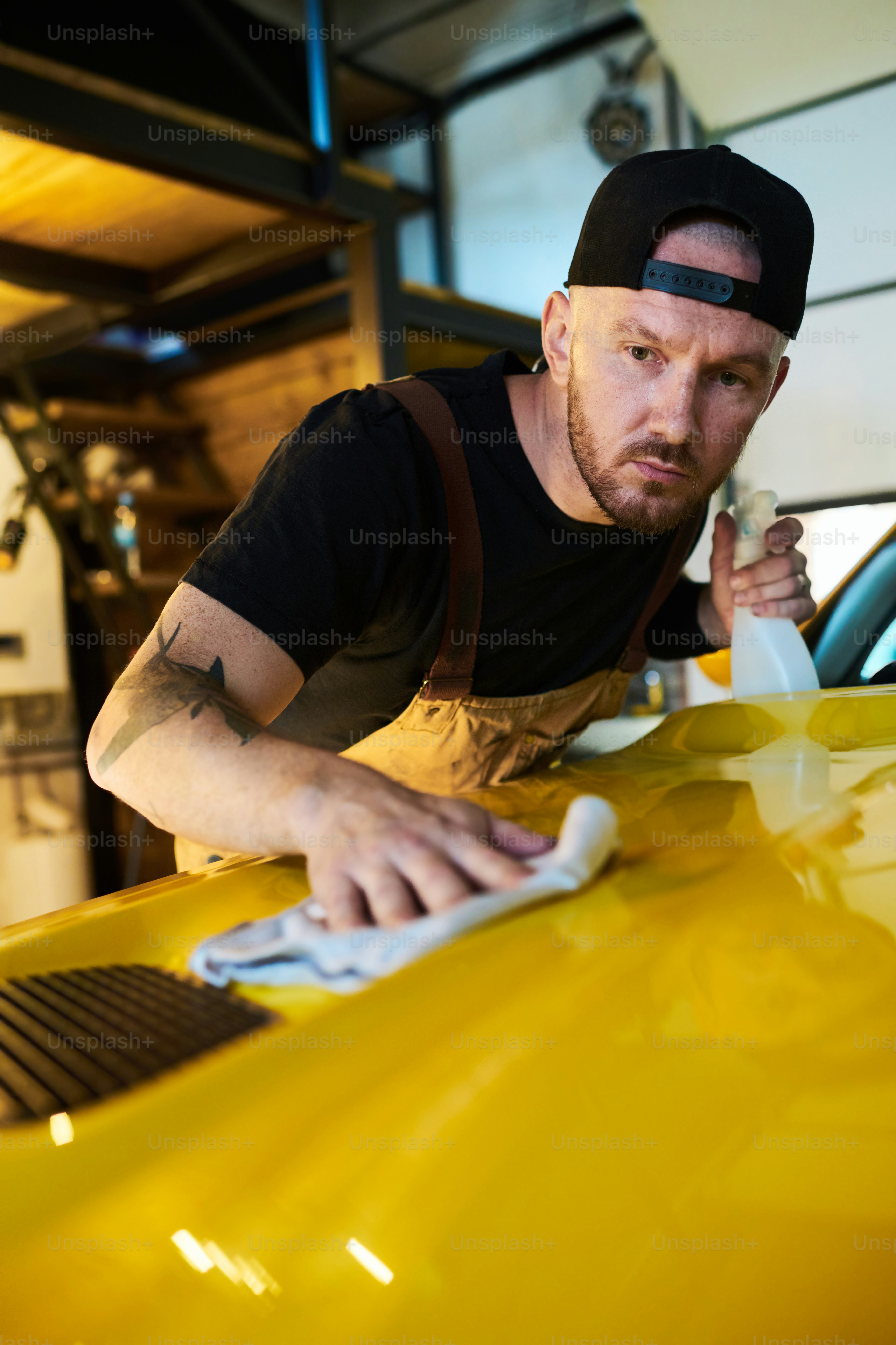Serious auto mechanic with flashlight bending over open hood of yellow ...