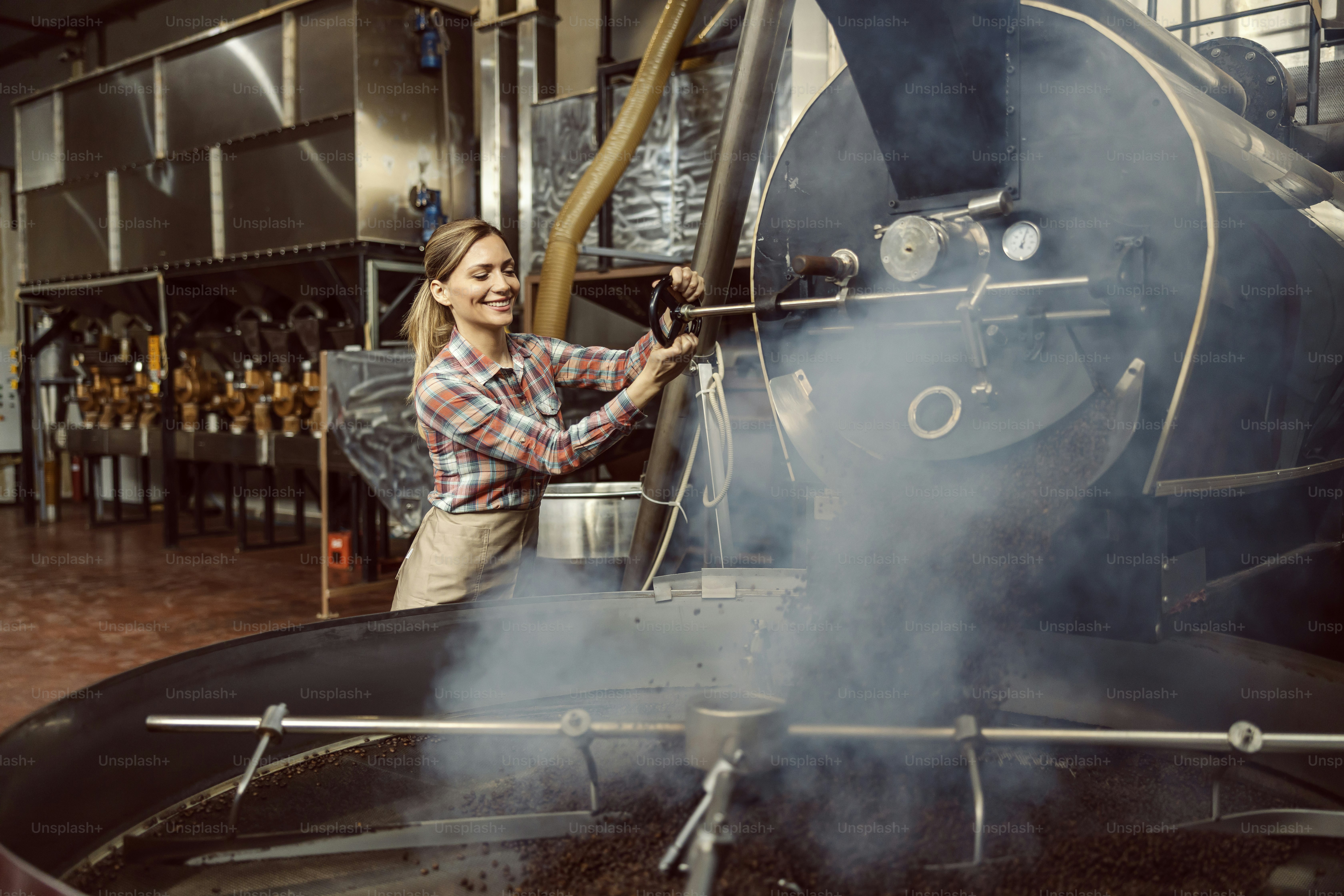 A female coffee factory worker operates coffee roasting machine in ...