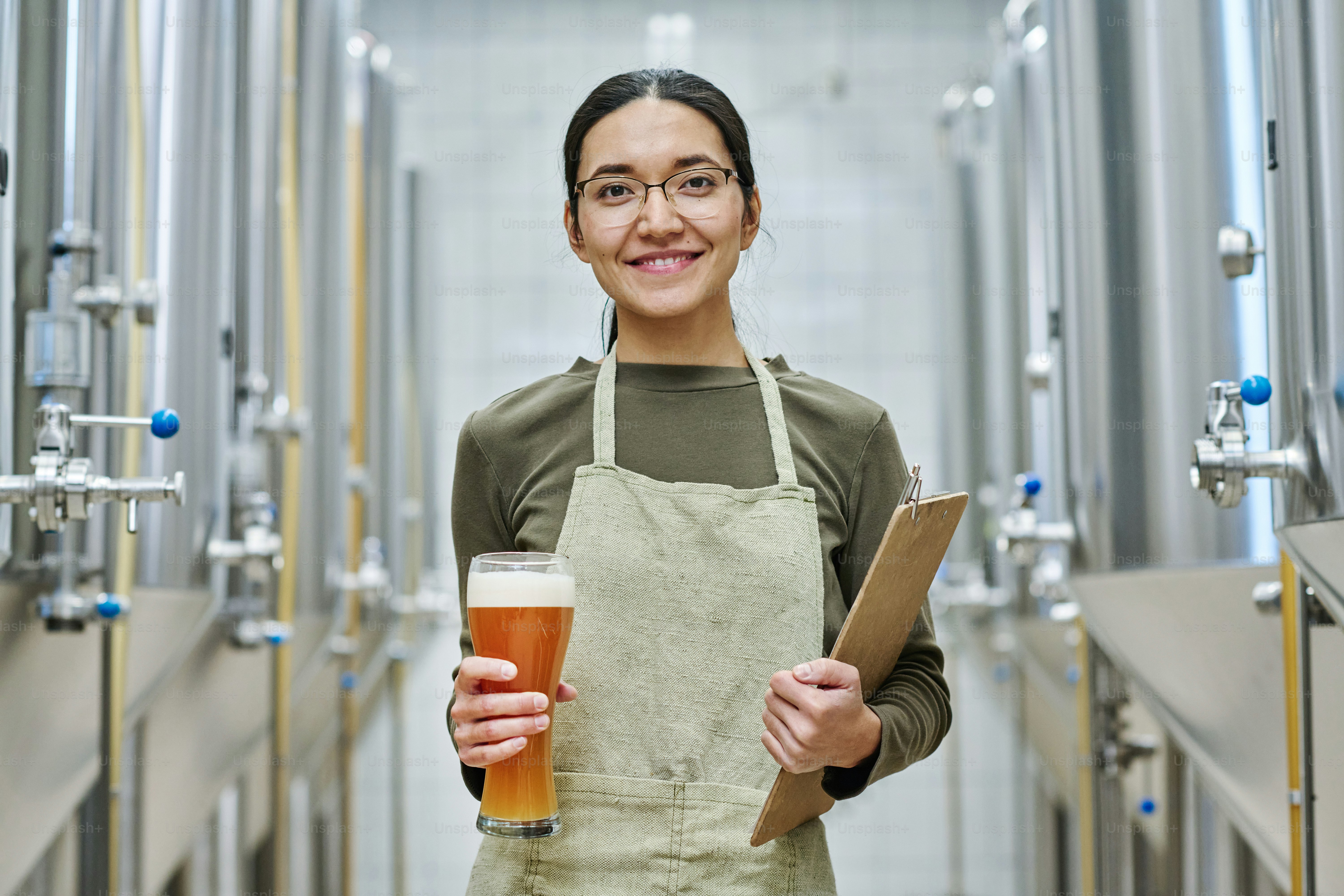 Portrait of young brewer smiling at camera while tasting fresh beer in ...