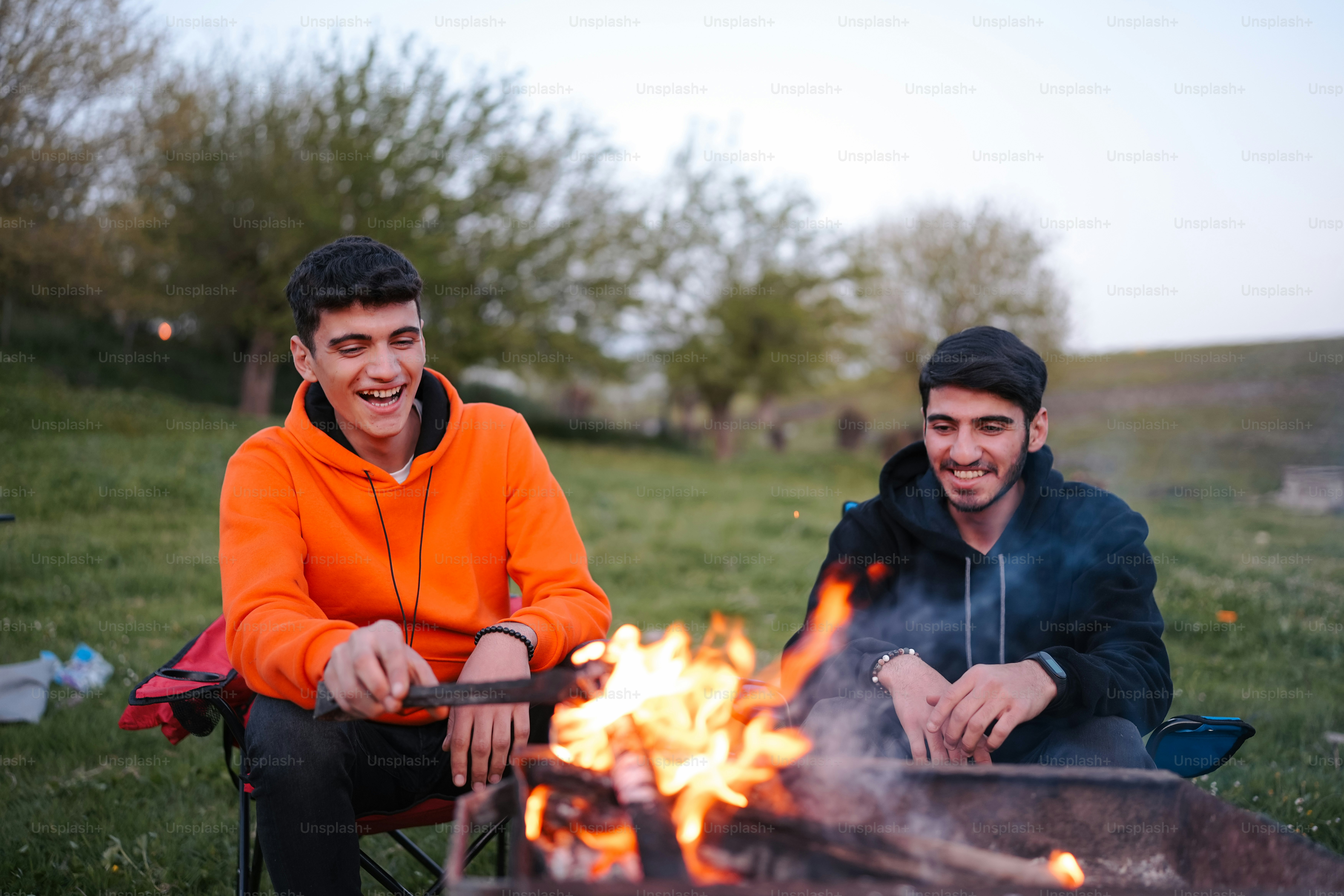 A couple of men sitting next to a fire photo – Eating outdoors Image on ...