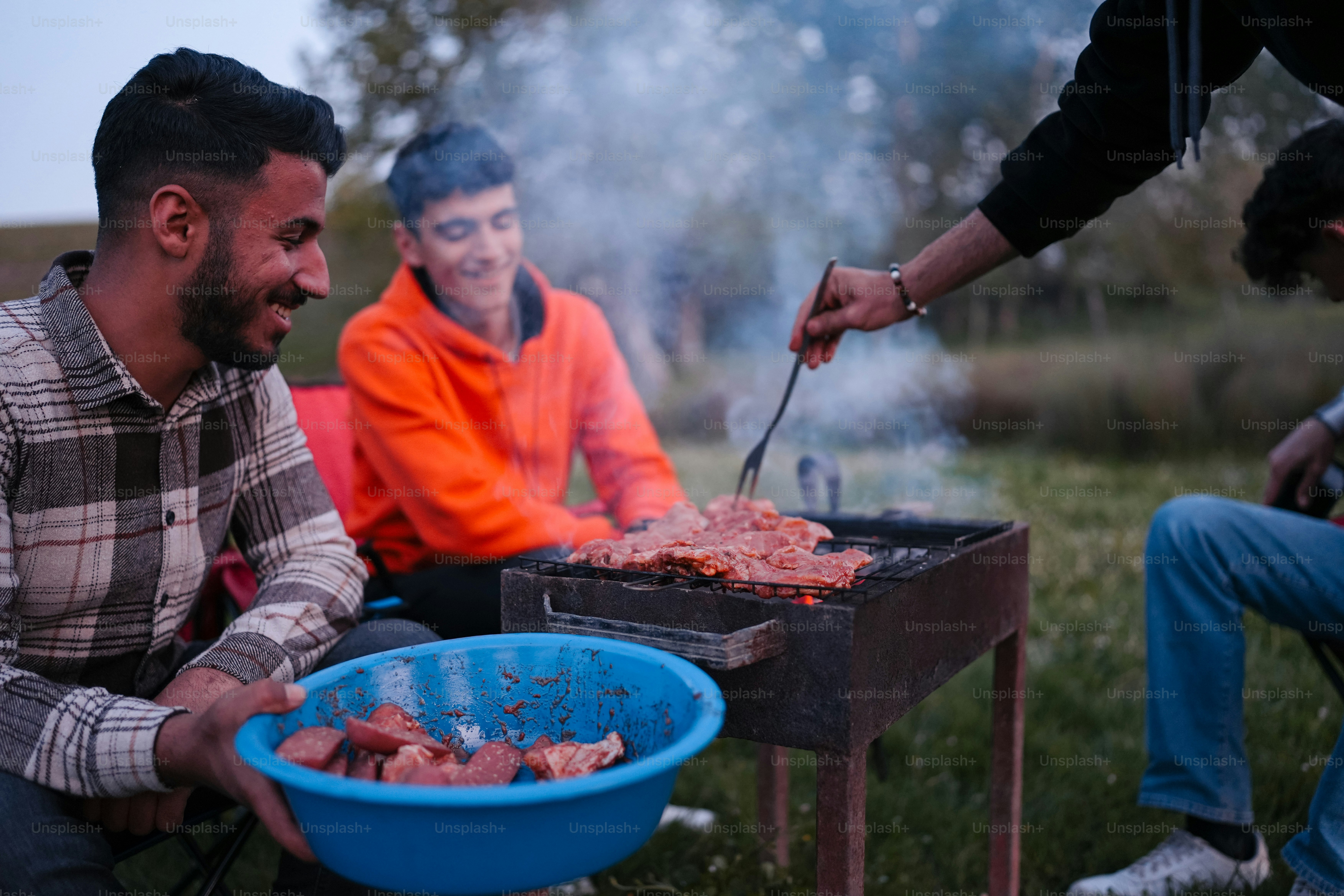 A group of people sitting around a bbq grill photo – Cooking over fire ...