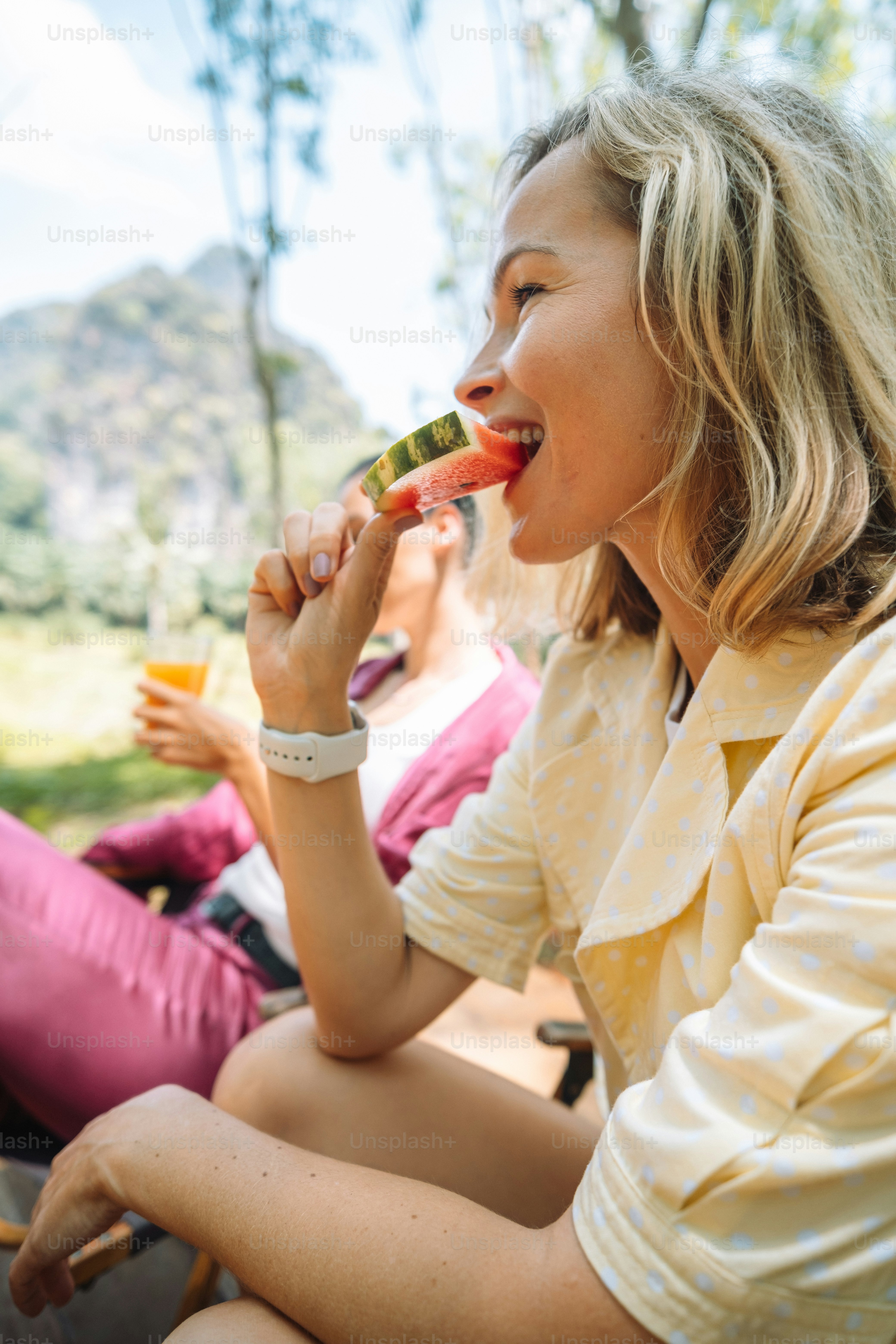 A woman sitting on the ground eating a slice of fruit photo – Party ...