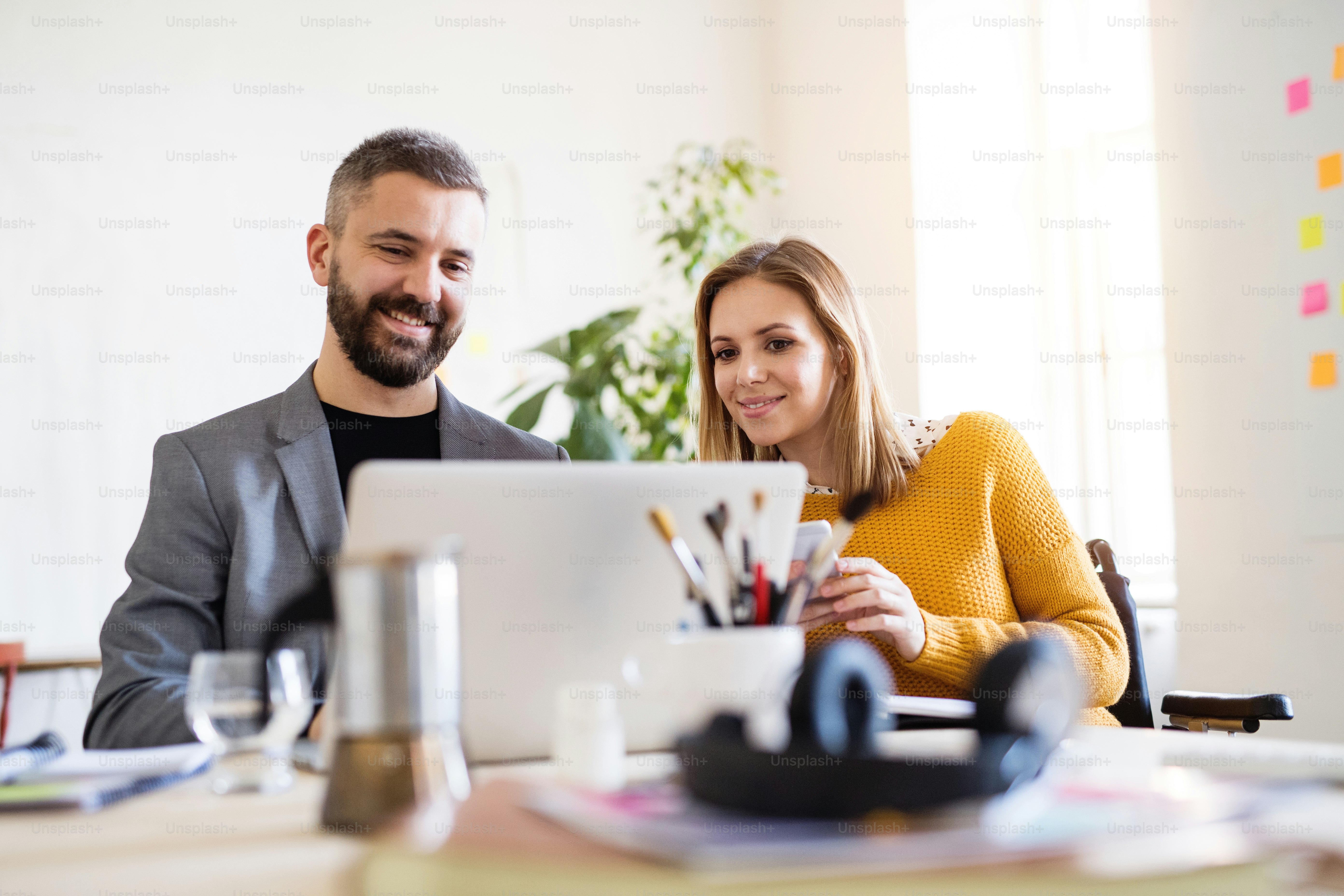 Two unrecognizable business people with wheelchair in the office working together. photo ...