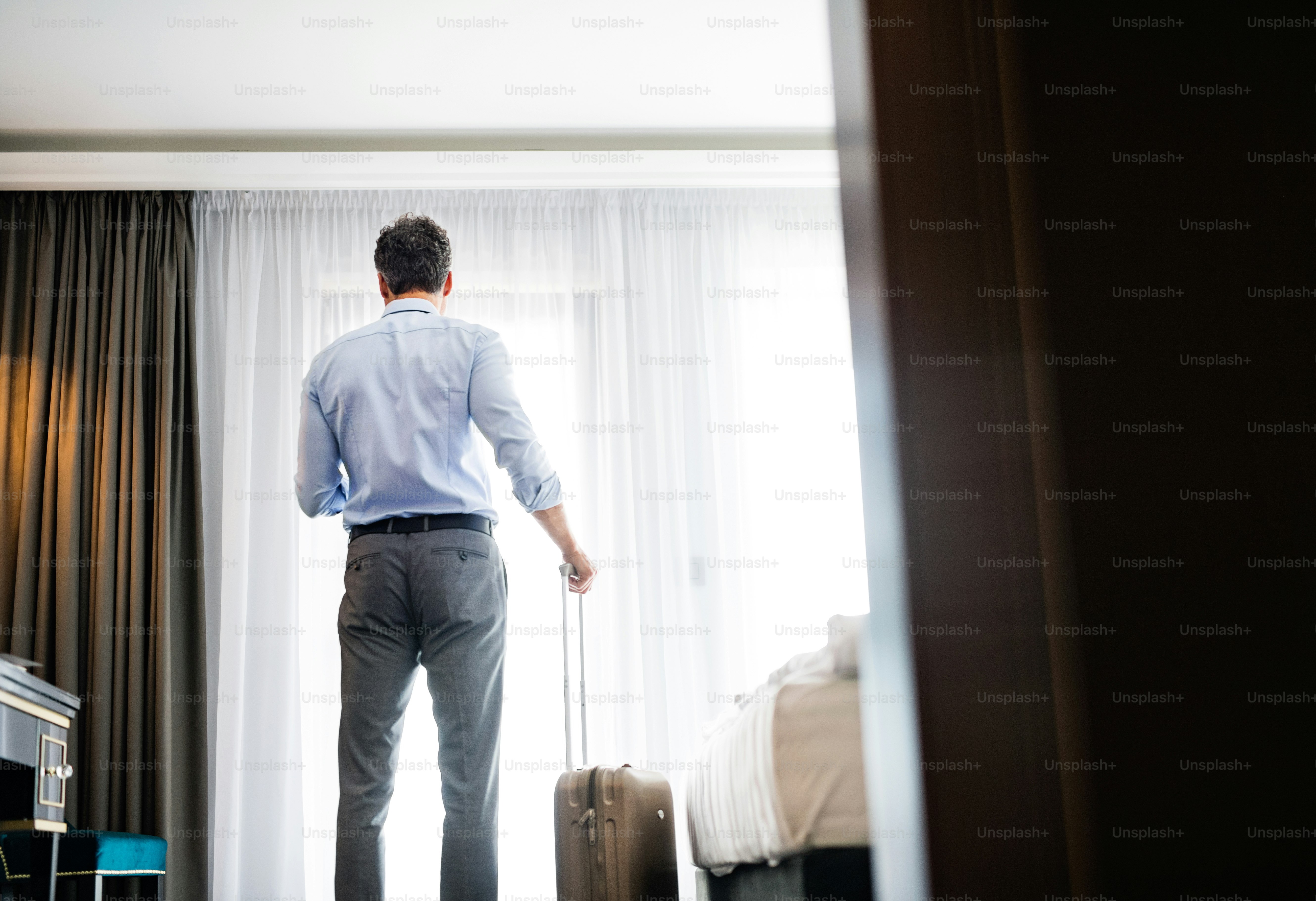 Mature businessman standing at the big windows in a hotel. Man looking ...