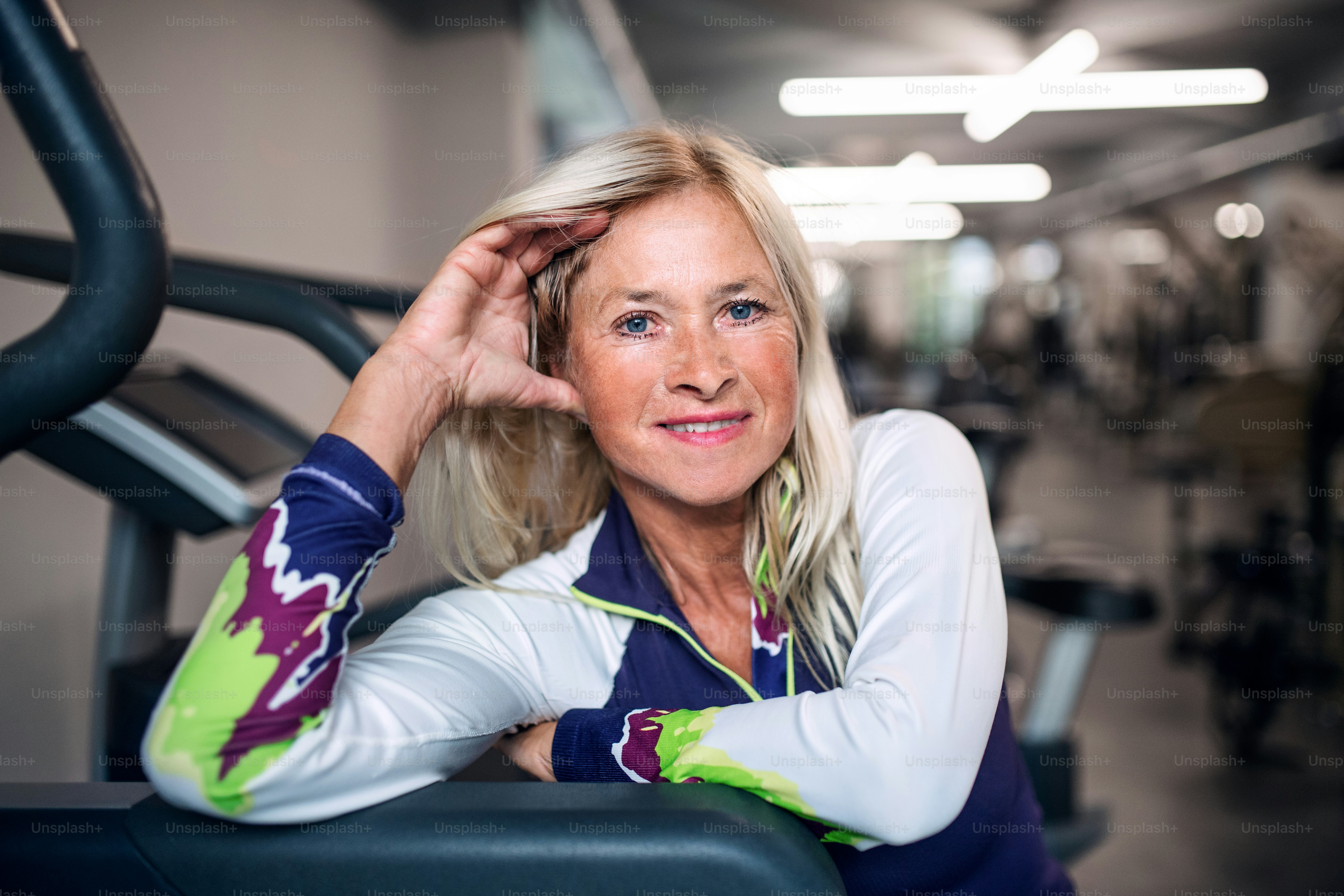 A front view of senior woman in gym resting after doing exercise ...