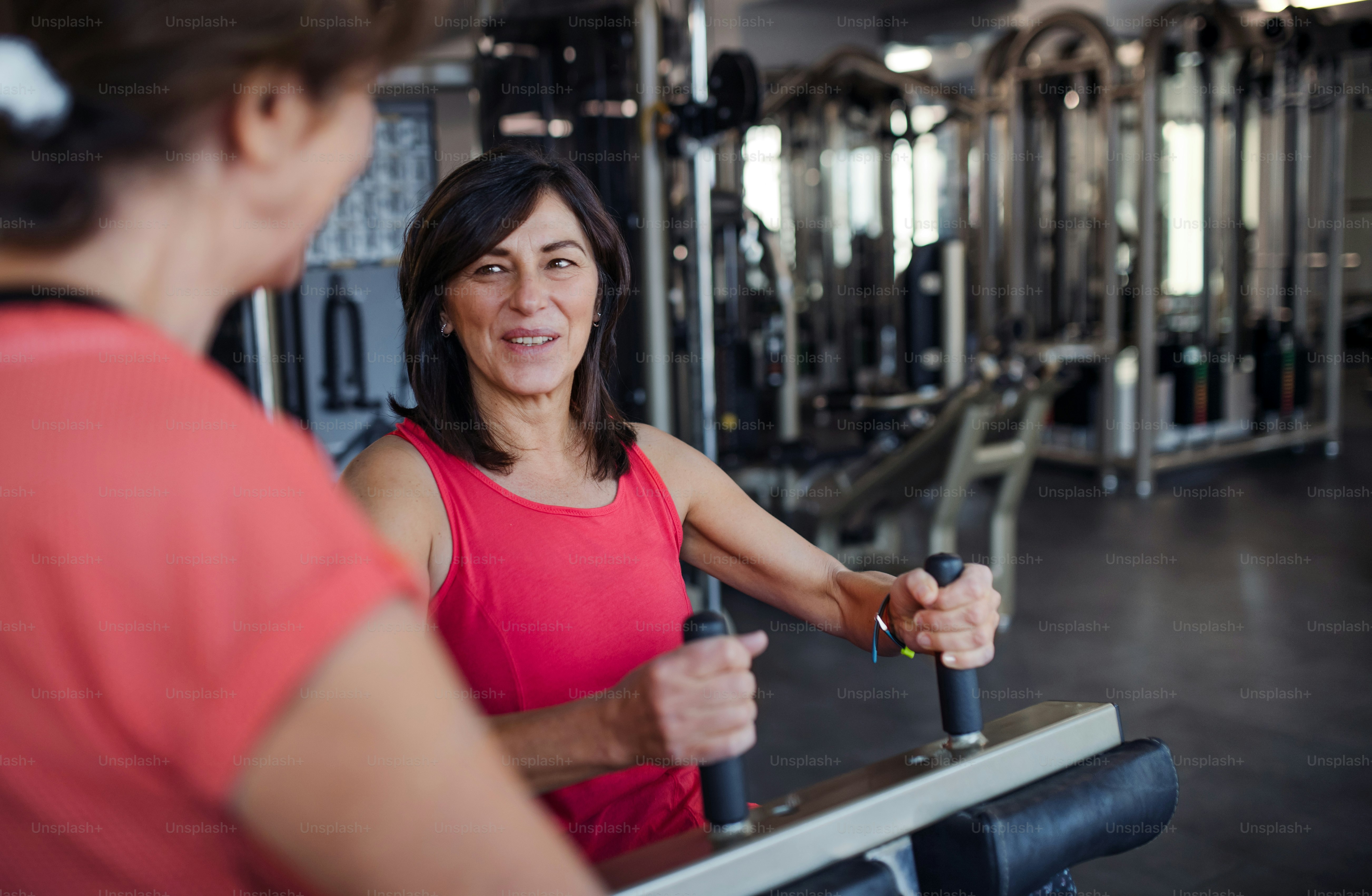 Two cheerful senior women friends in gym doing strength workout ...