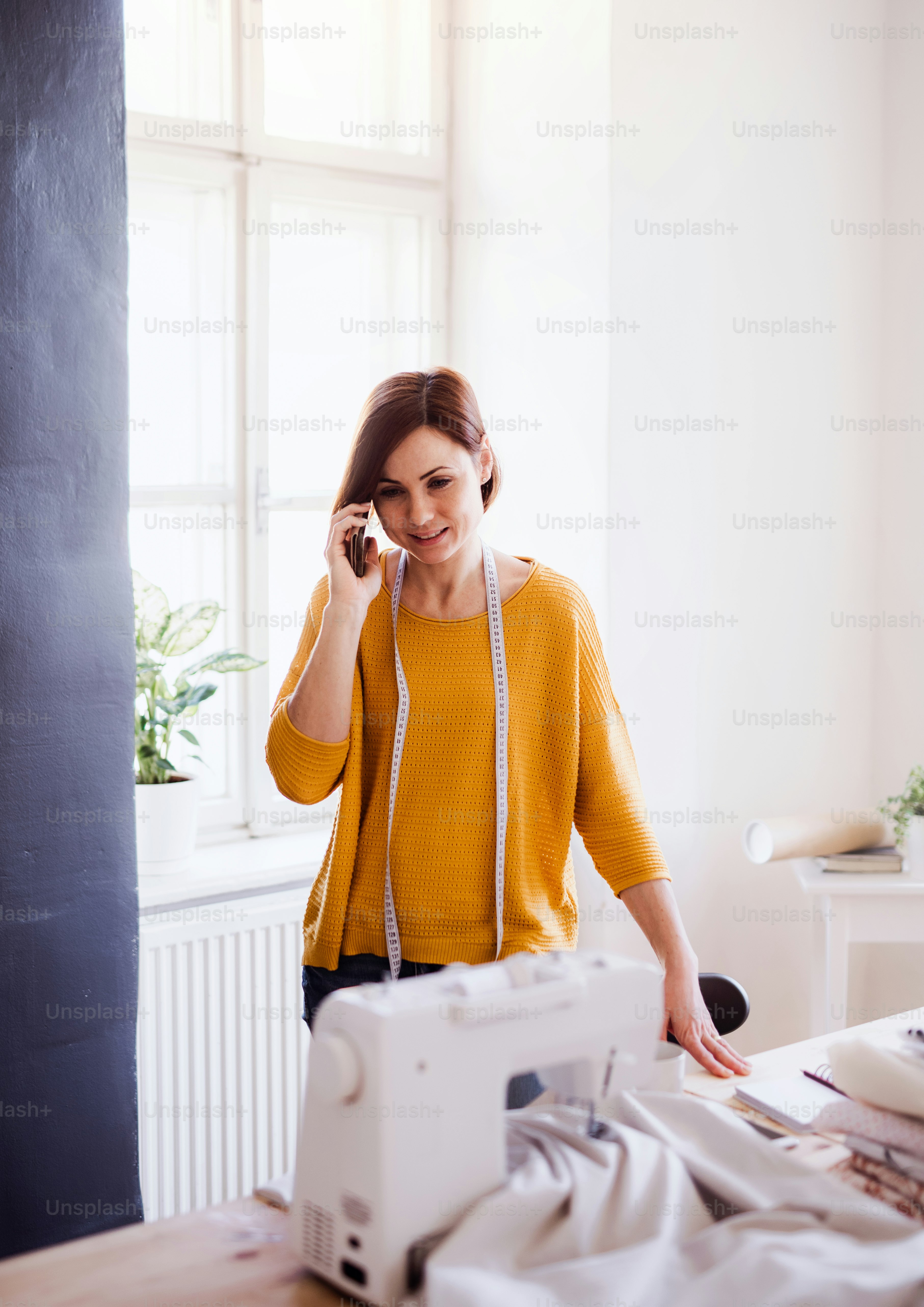 Young creative woman in a studio, using smartphone. A startup of small tailoring business. Copy ...